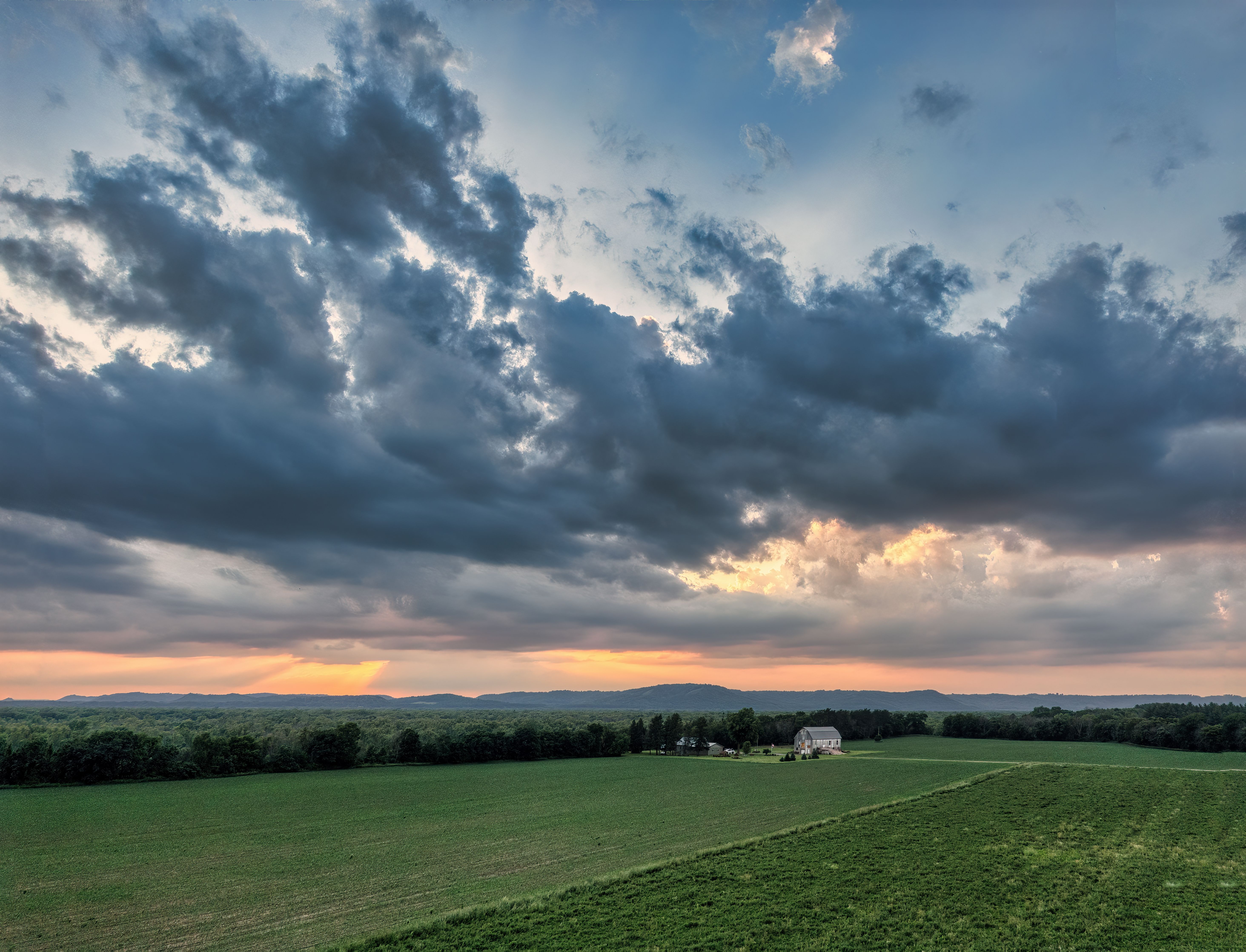 A cloudy sky over a field with a farm and a barn · Free Stock Photo