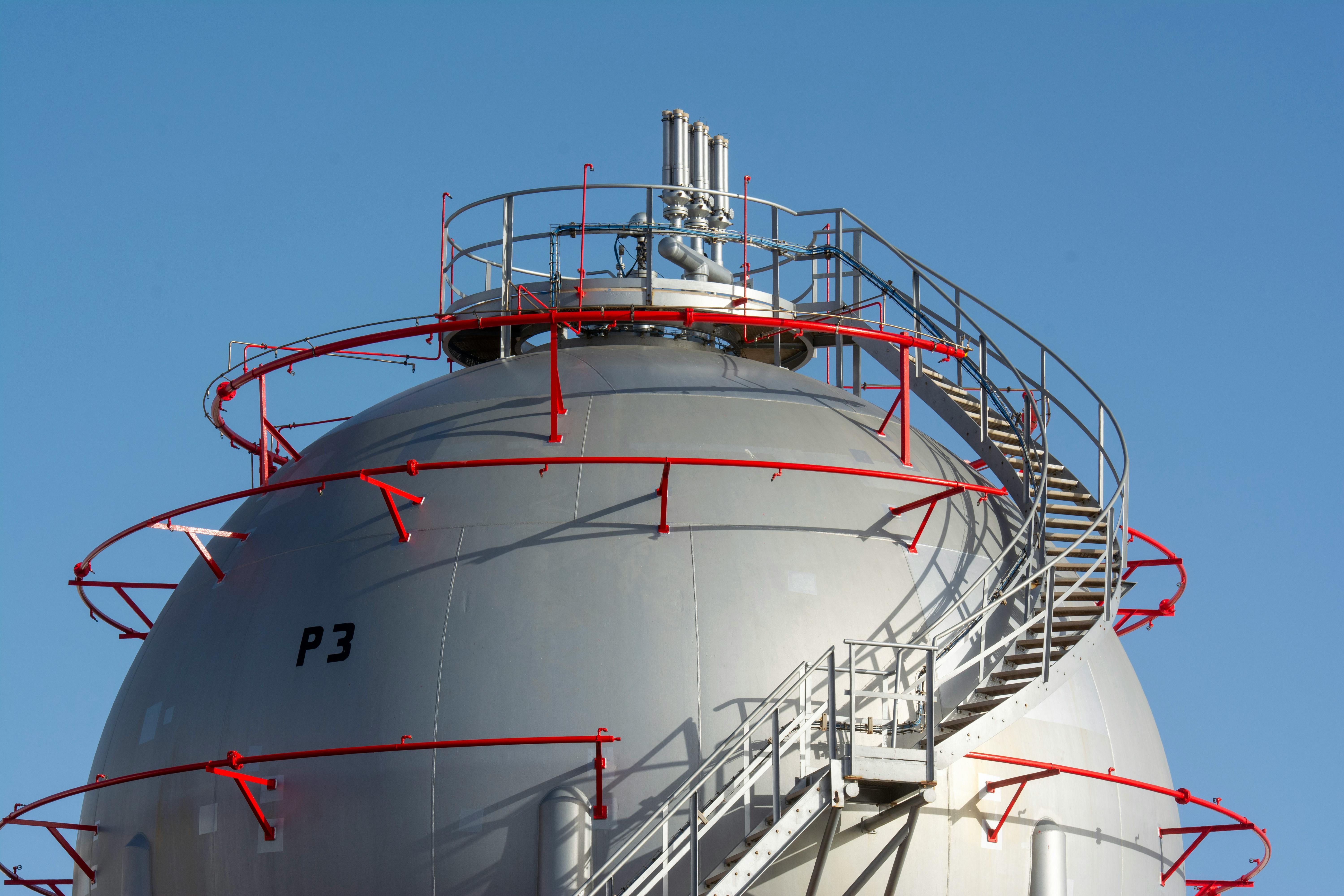 A large steel tank with red stairs and a blue sky · Free Stock Photo