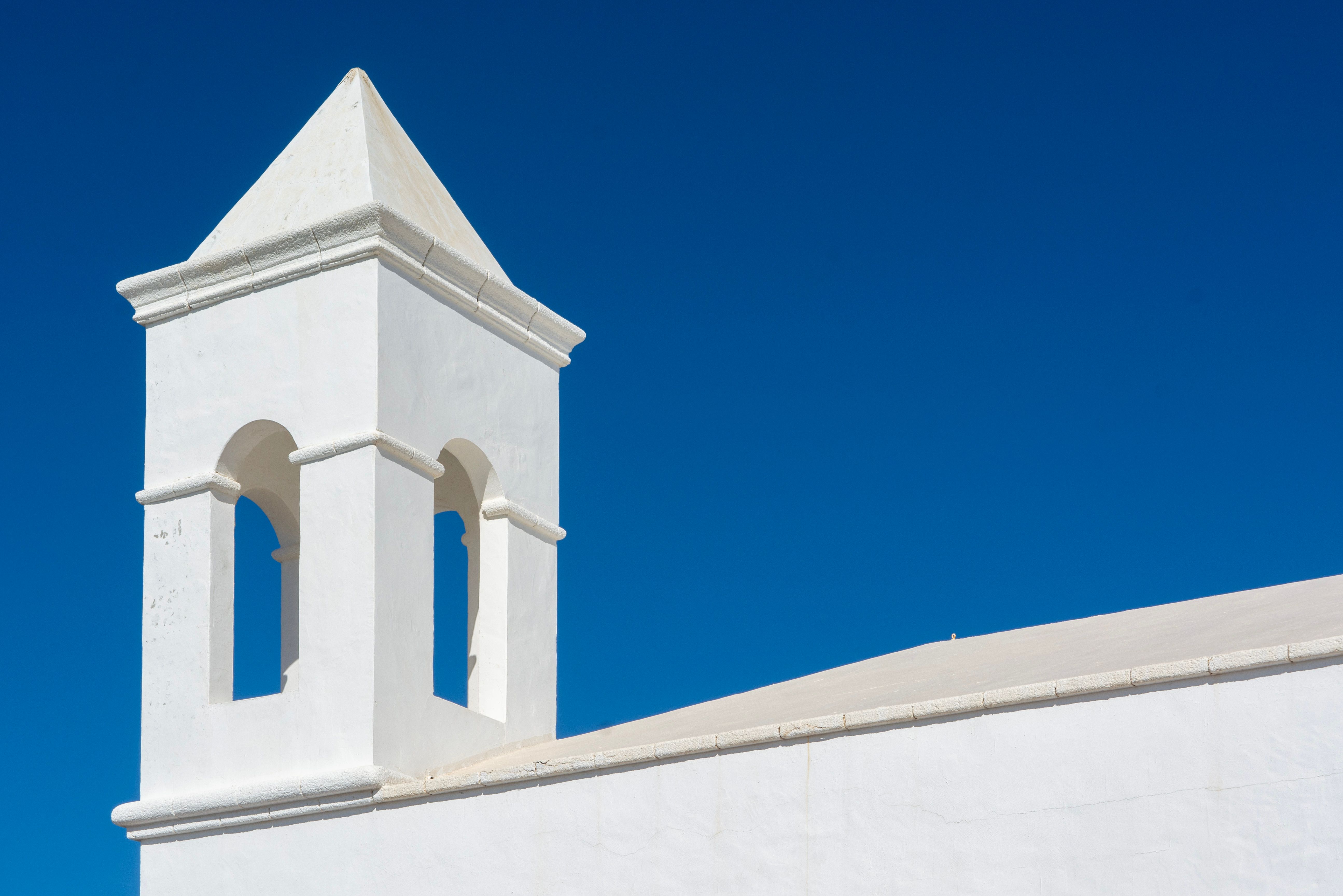 A white church tower with a blue sky in the background · Free Stock Photo