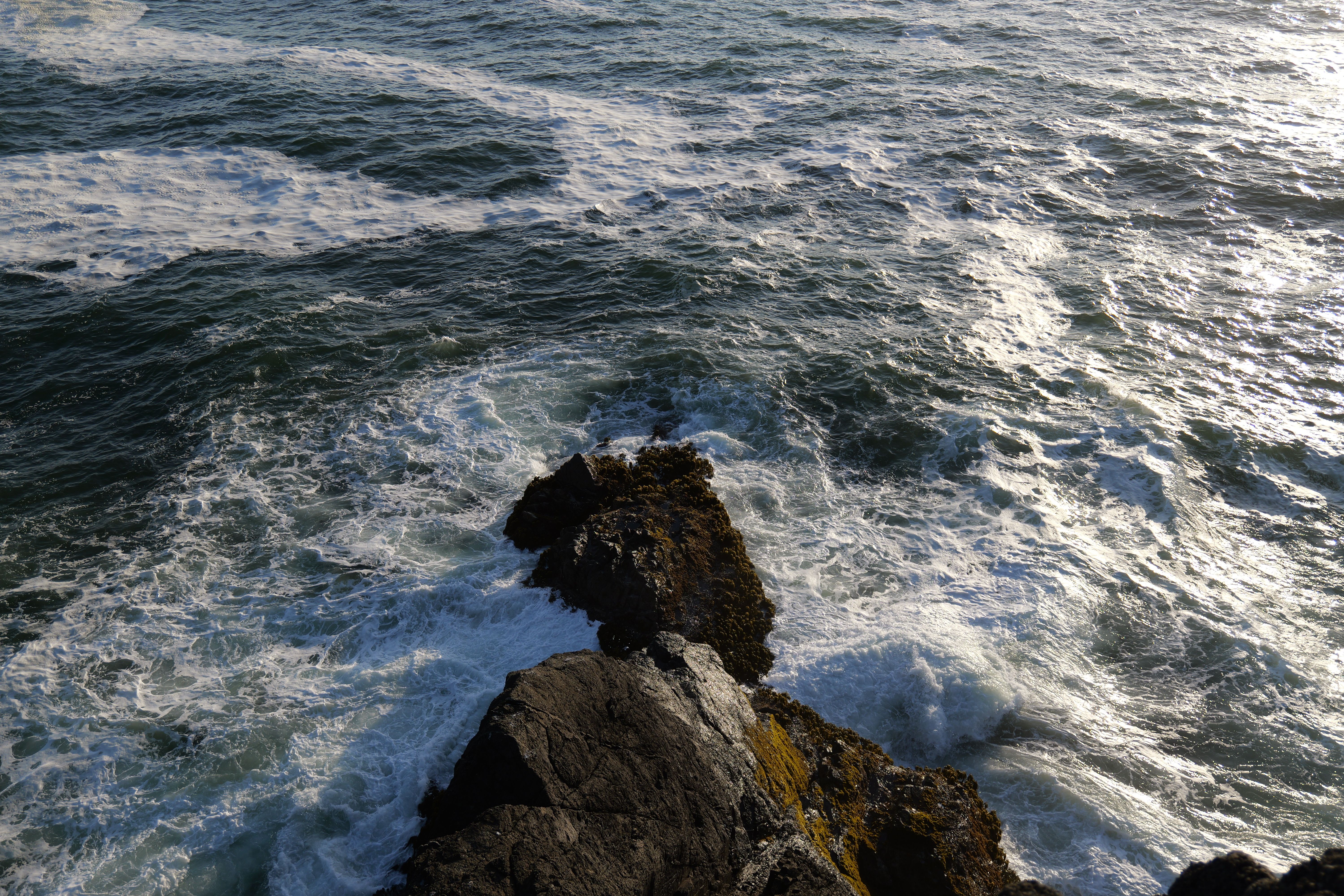 A person standing on the edge of a cliff looking out at the ocean ...