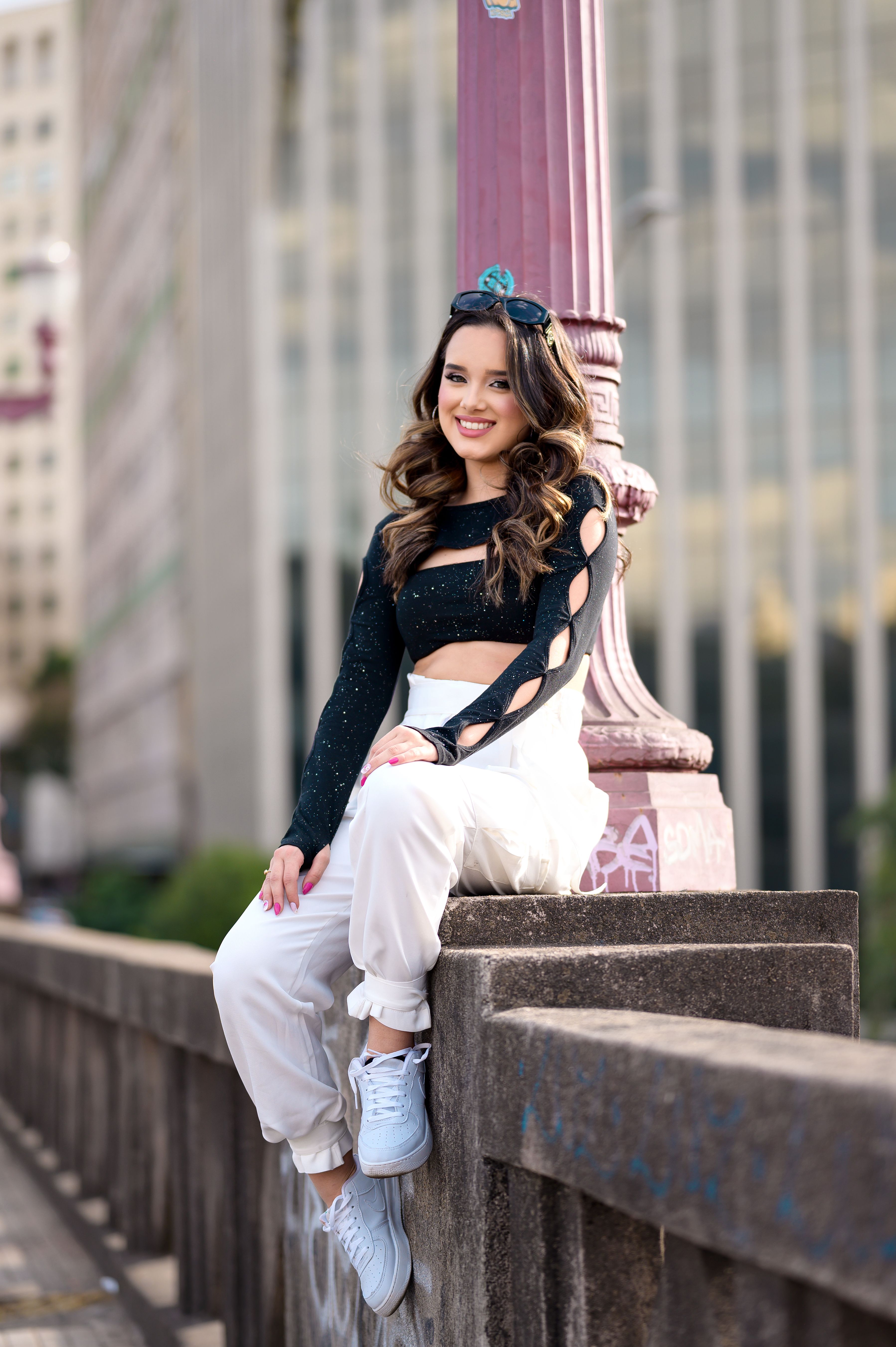 A young woman sitting on a ledge in front of a bridge · Free Stock Photo