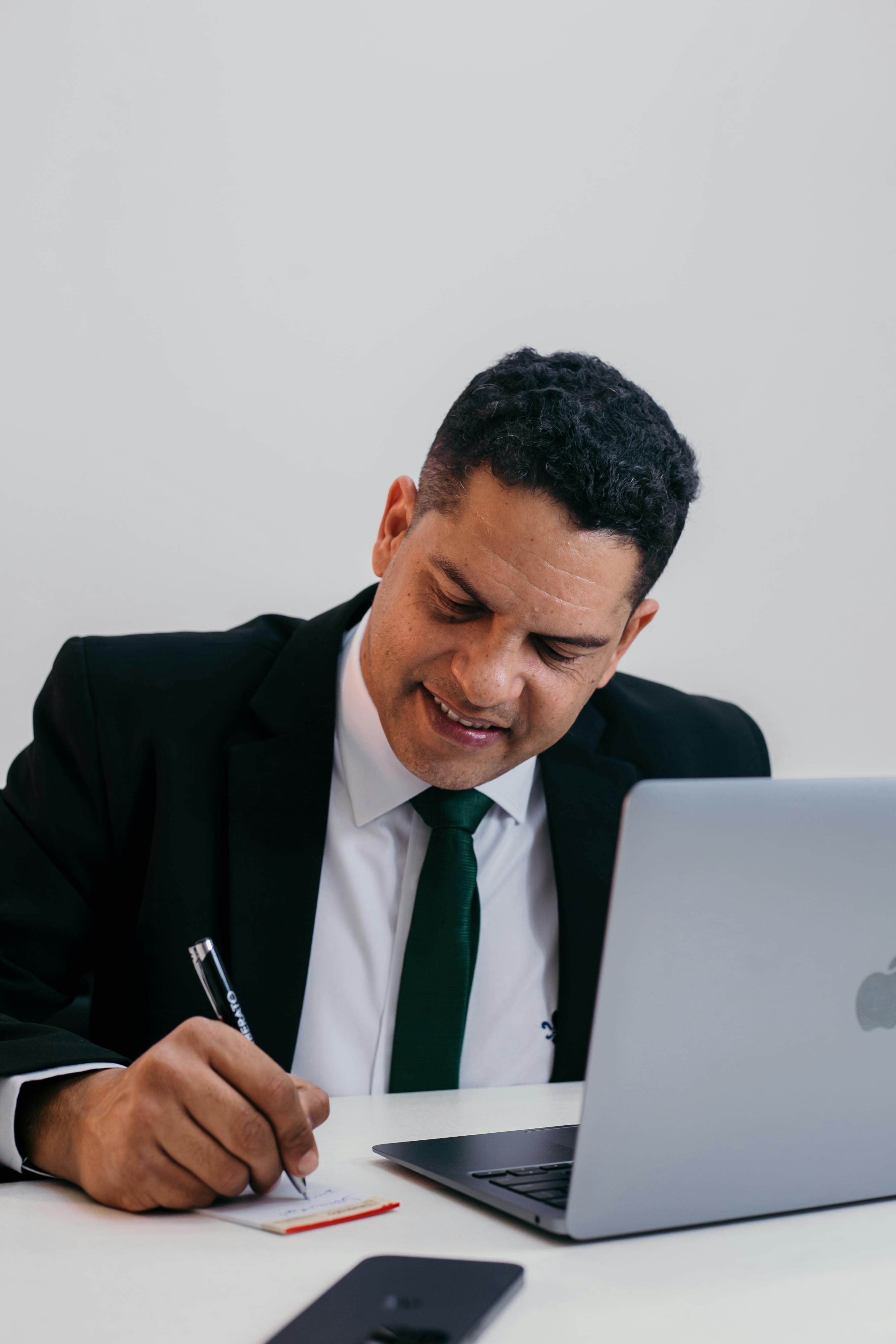 Man in Suit Writing and Working on Laptop · Free Stock Photo