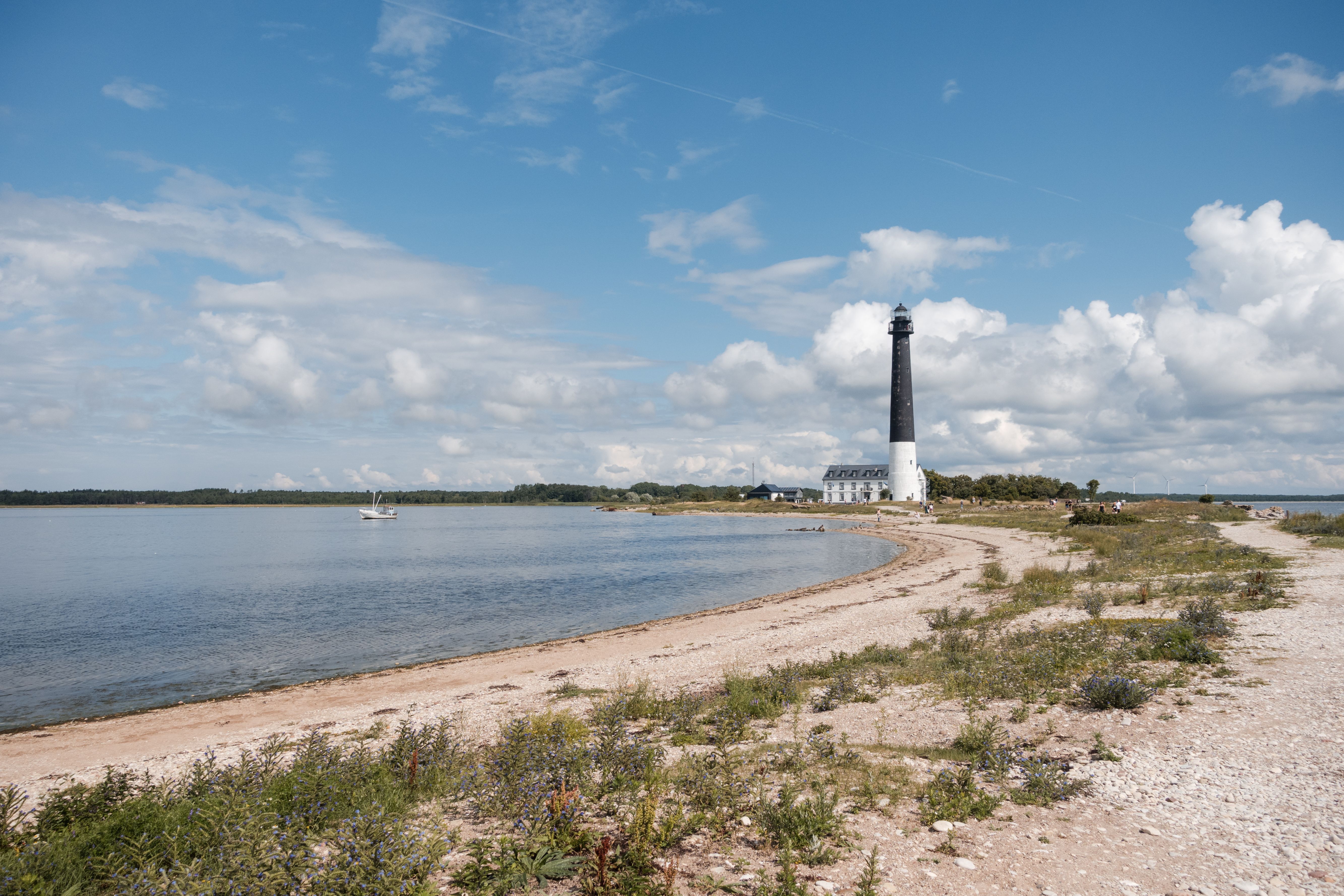 A lighthouse sits on a sandy beach near the water · Free Stock Photo