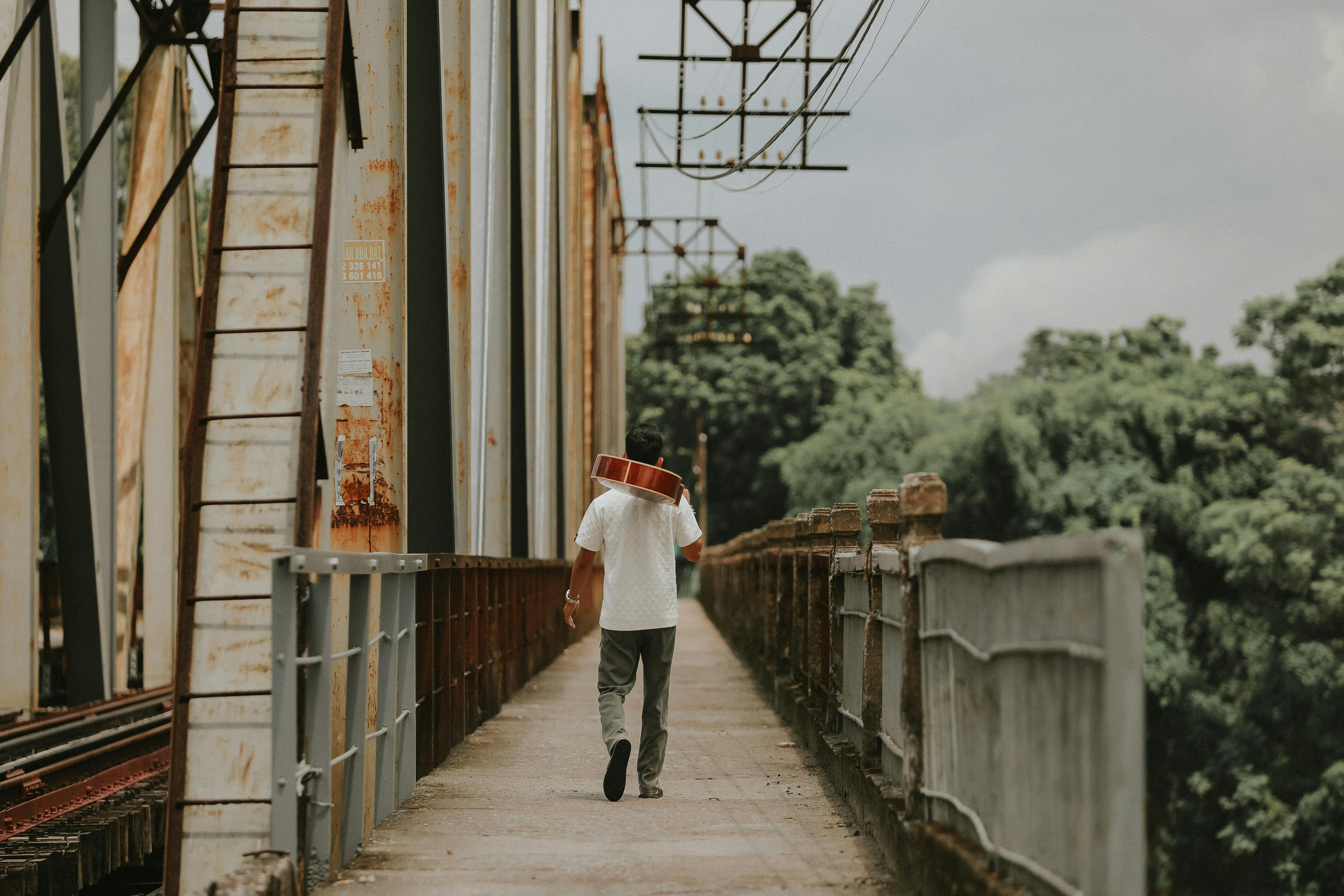 A man walking on a bridge with a red hat · Free Stock Photo