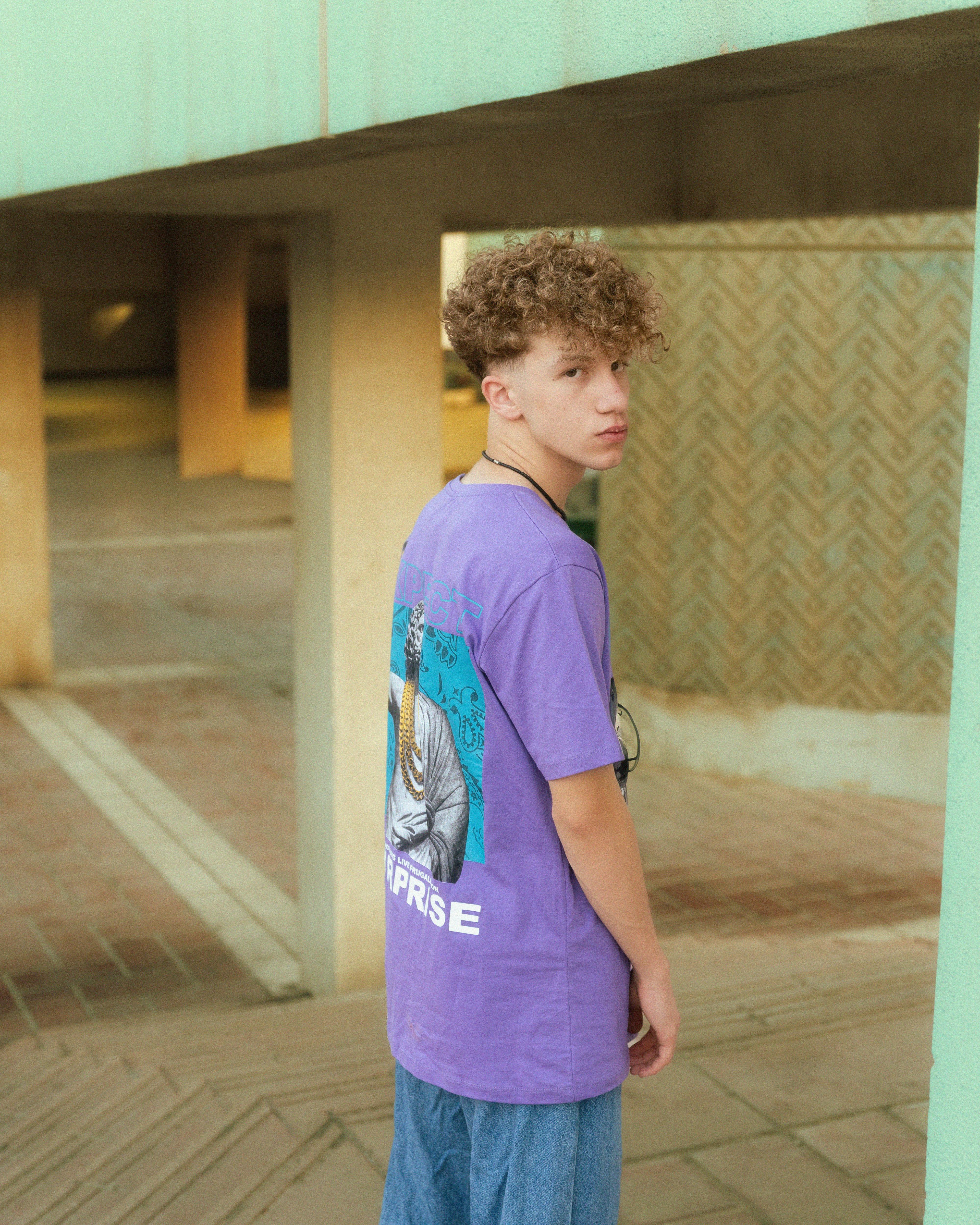 A young man in purple shirt and jeans standing in front of a building ...