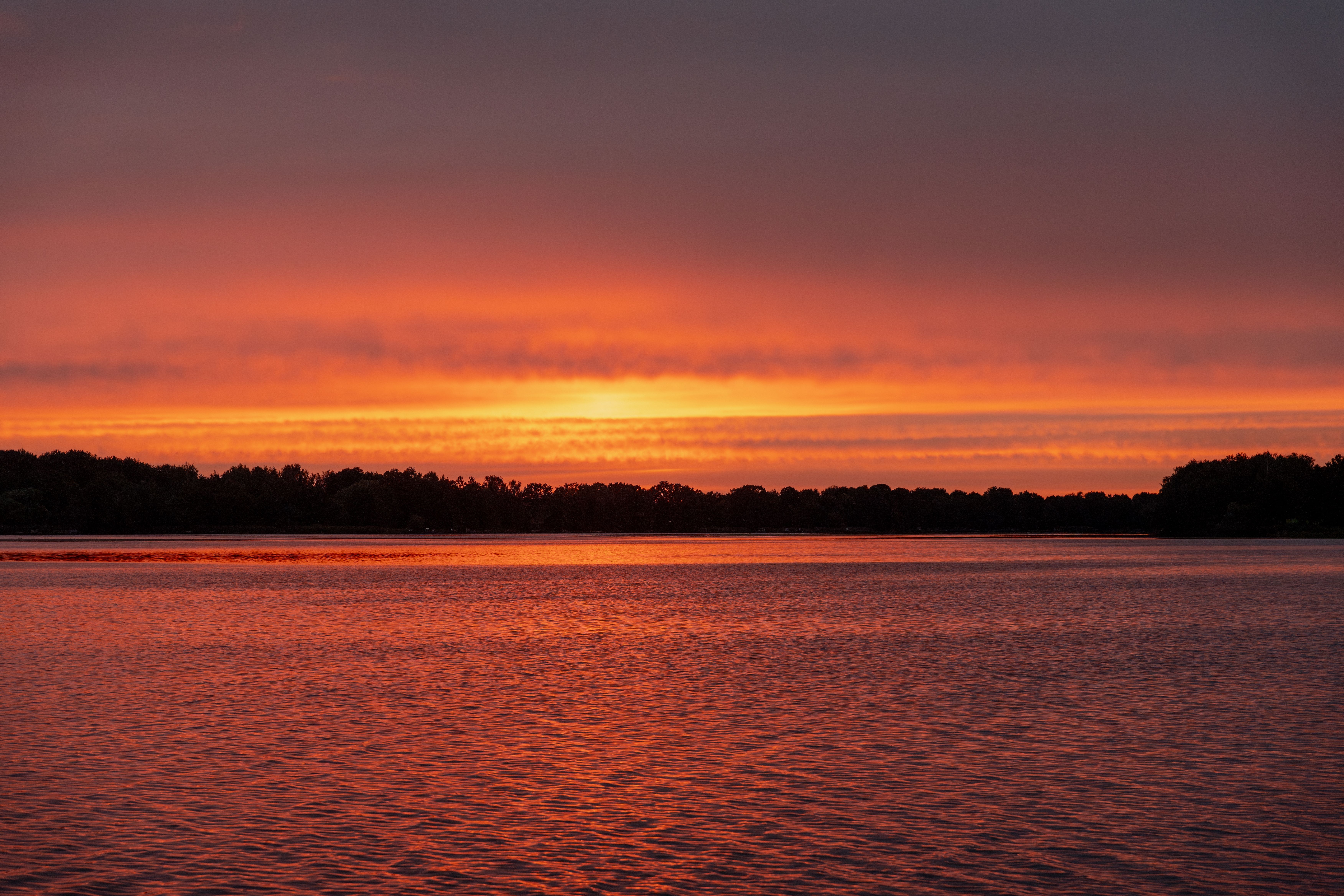 A sunset over a lake with clouds in the sky · Free Stock Photo