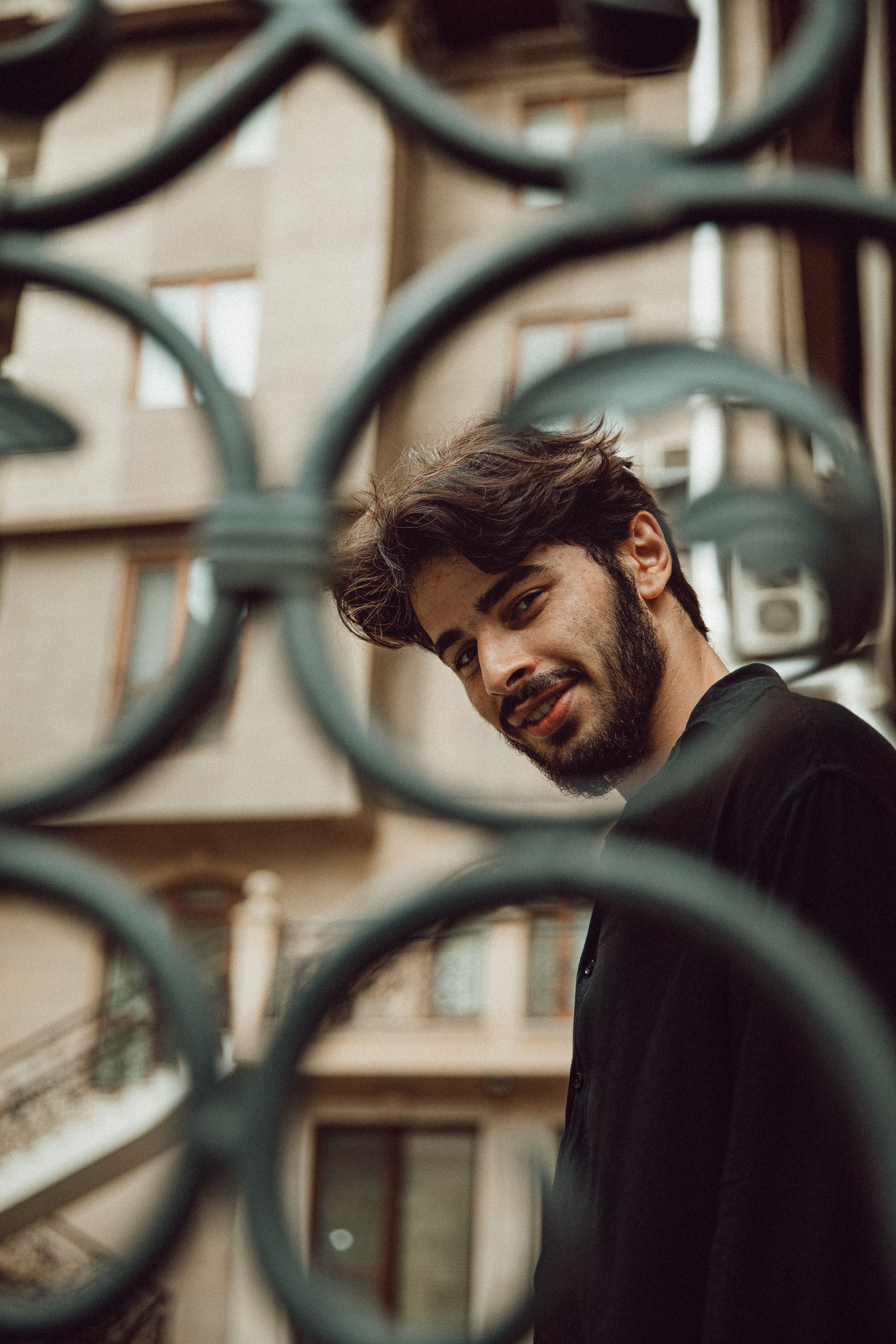 A man with a beard looking through a metal gate · Free Stock Photo