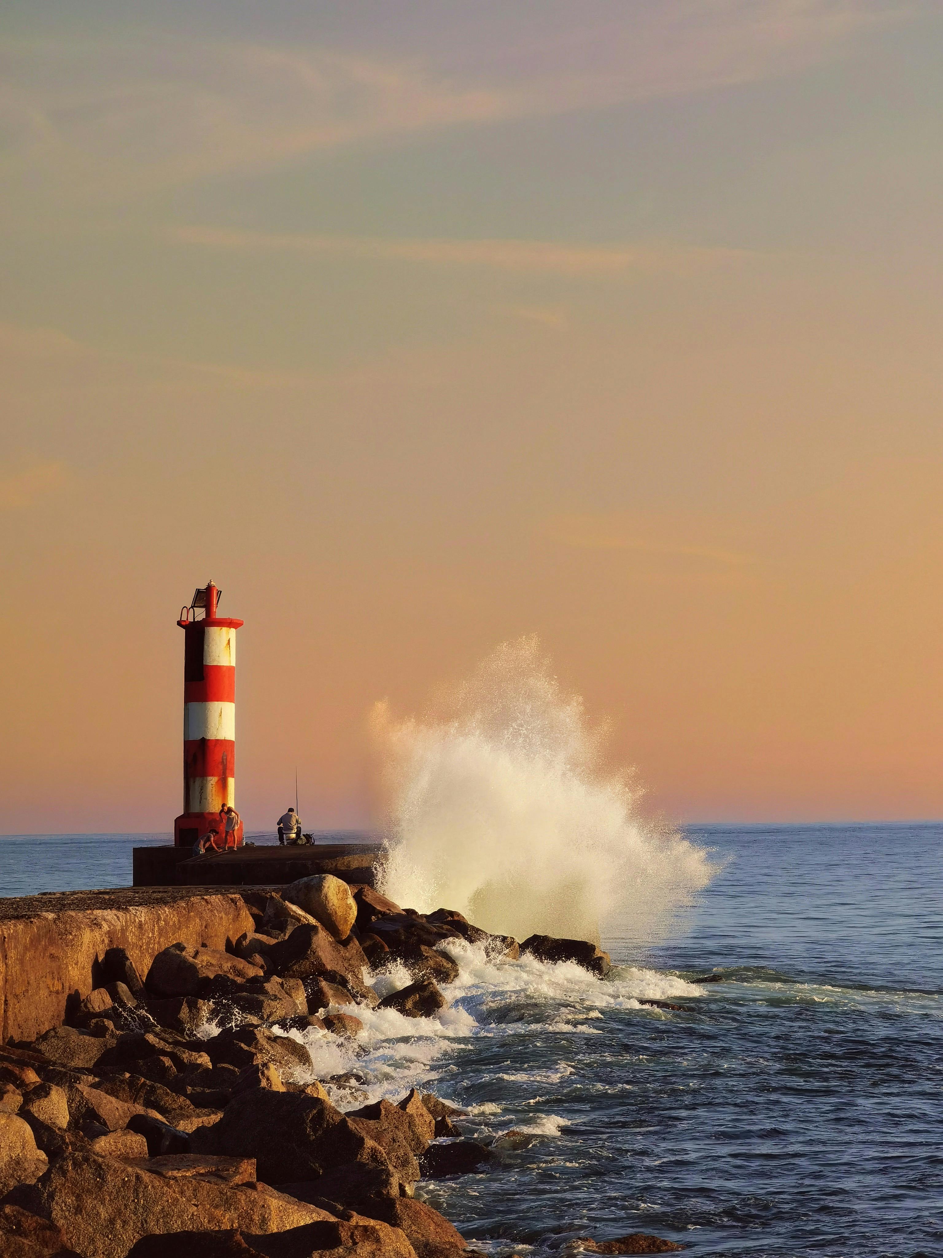 A lighthouse is in the ocean with waves crashing · Free Stock Photo