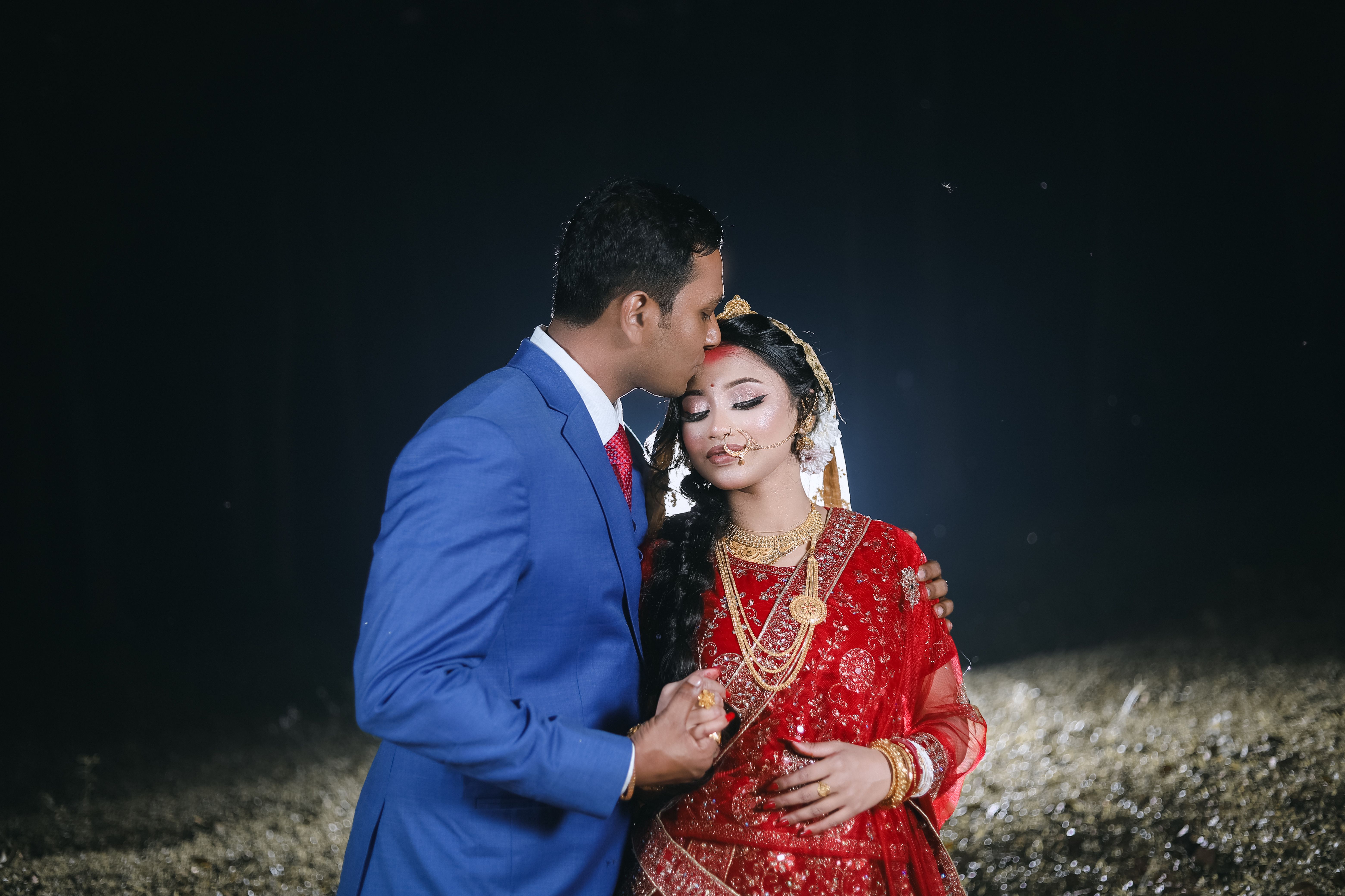 A bride and groom in red and blue outfits standing in the dark · Free ...