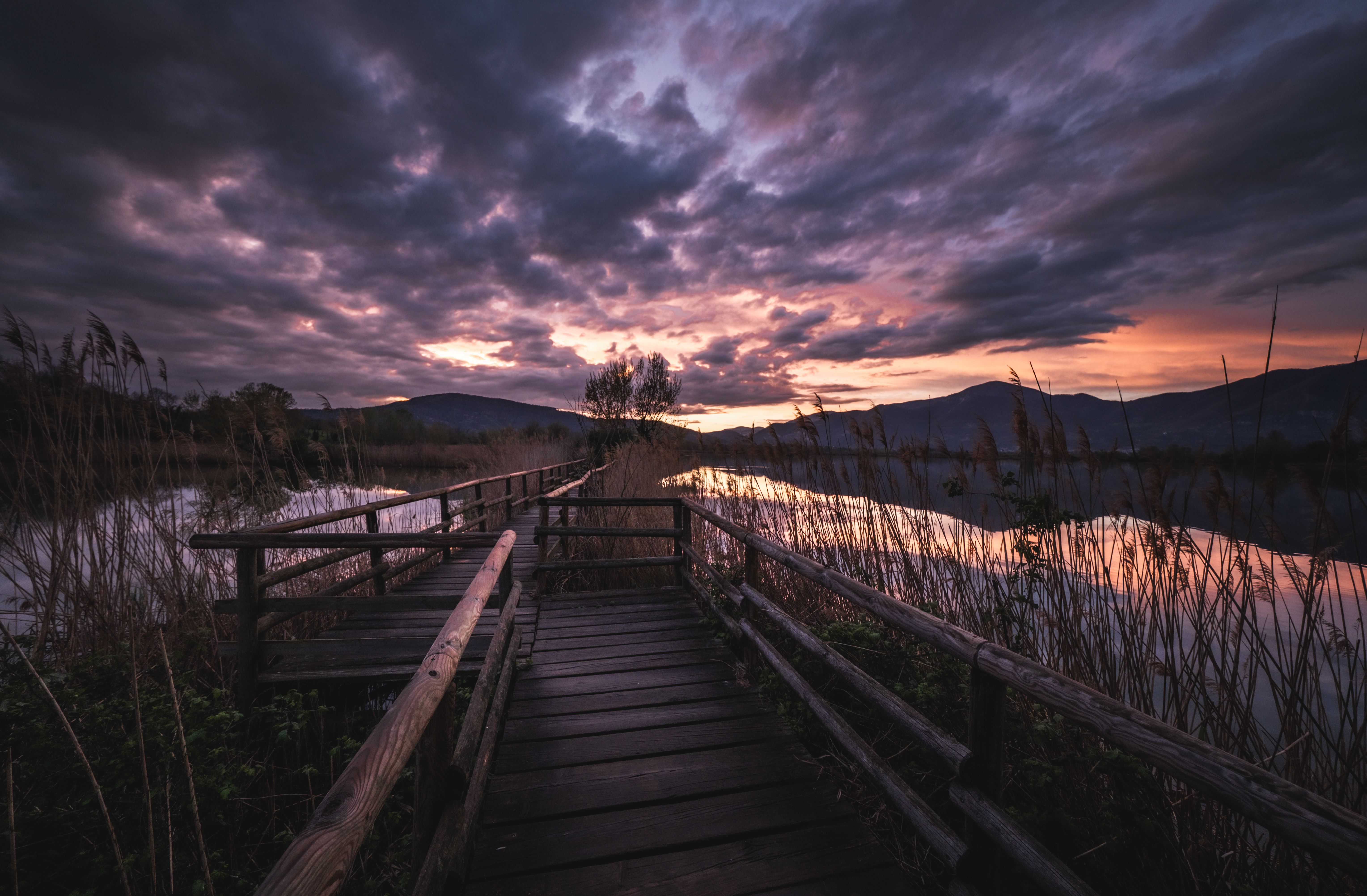 A wooden walkway leading to a lake at sunset · Free Stock Photo
