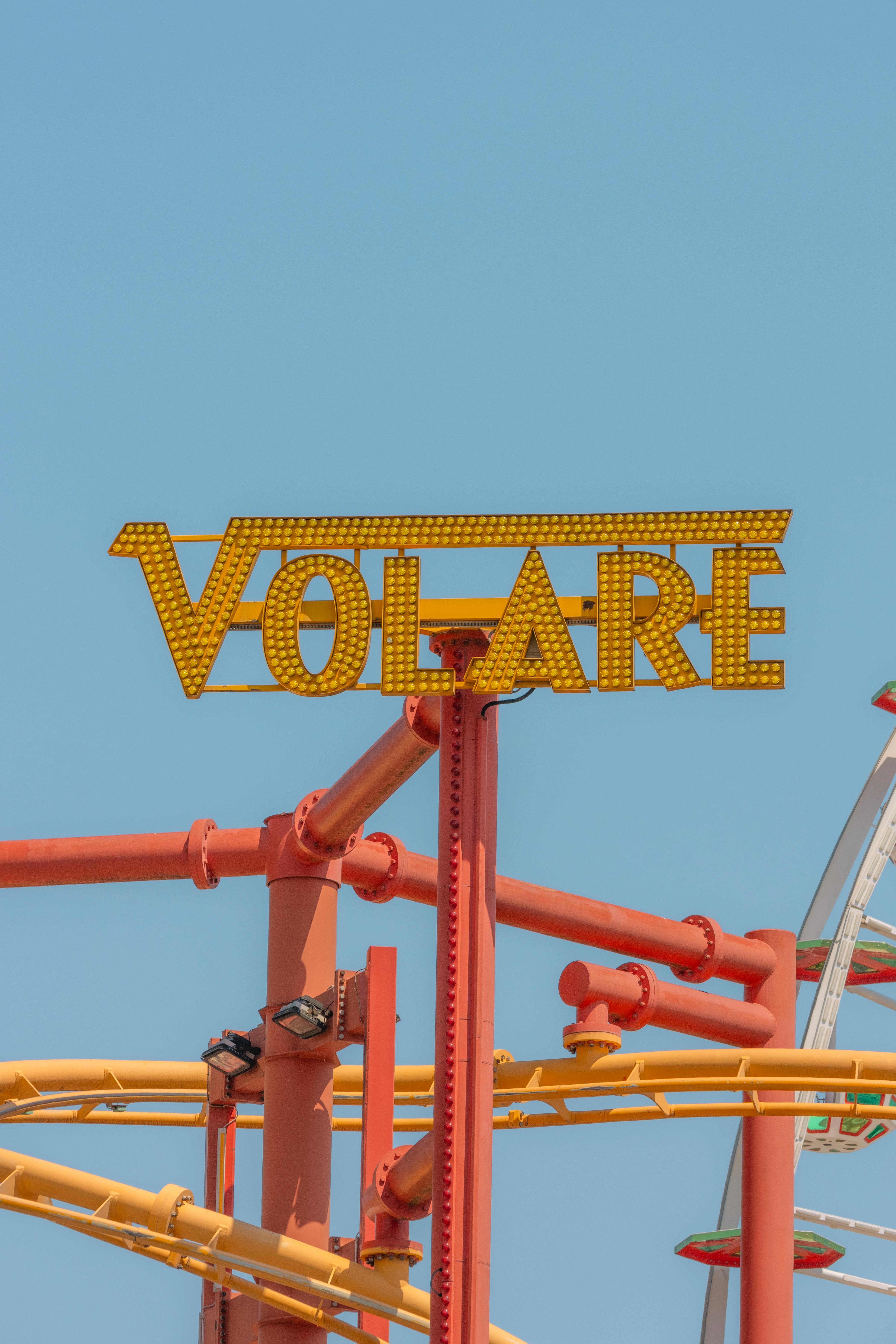 A sign that says volare with a ferris wheel in the background · Free ...