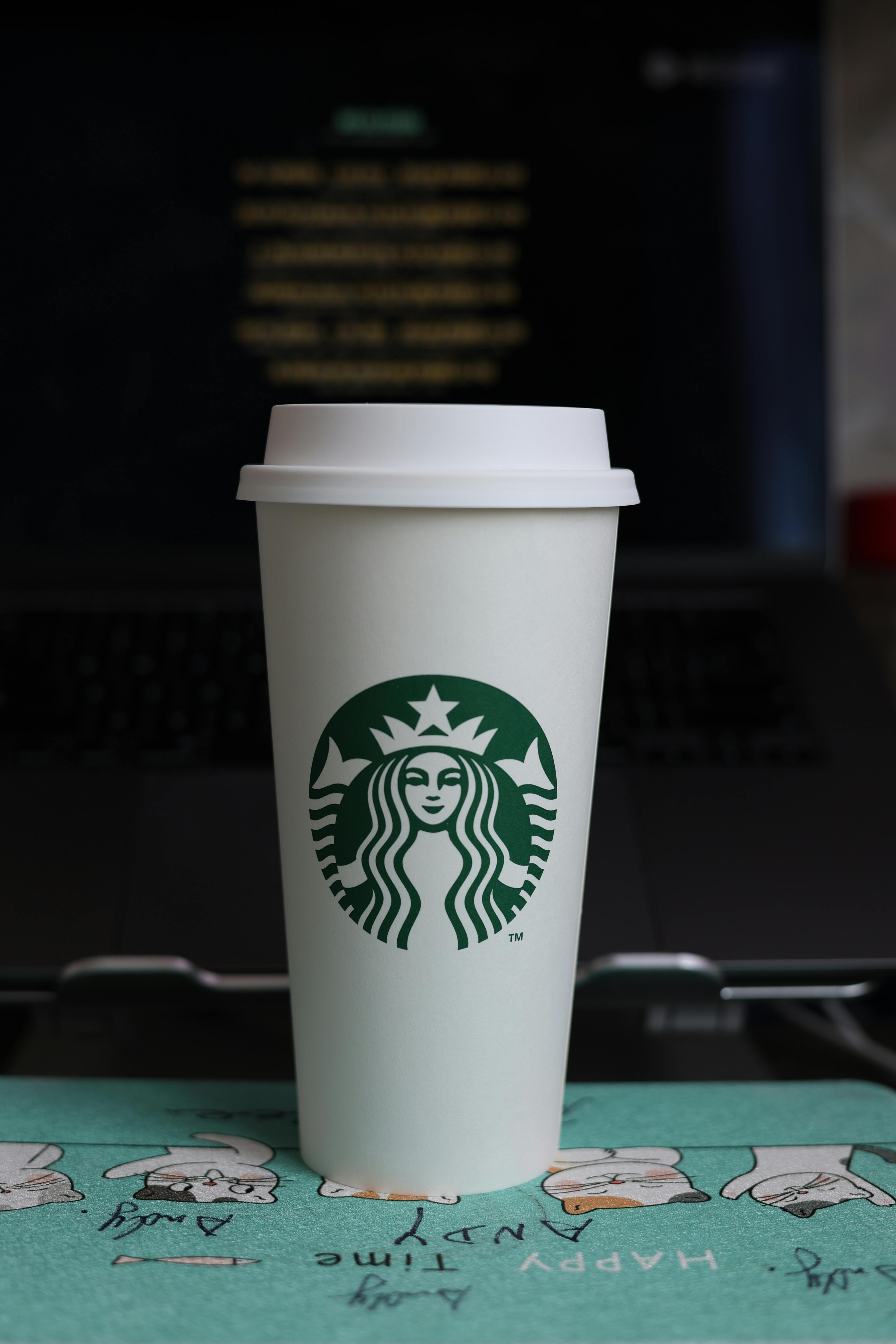 Starbucks coffee cup on a table next to a laptop · Free Stock Photo