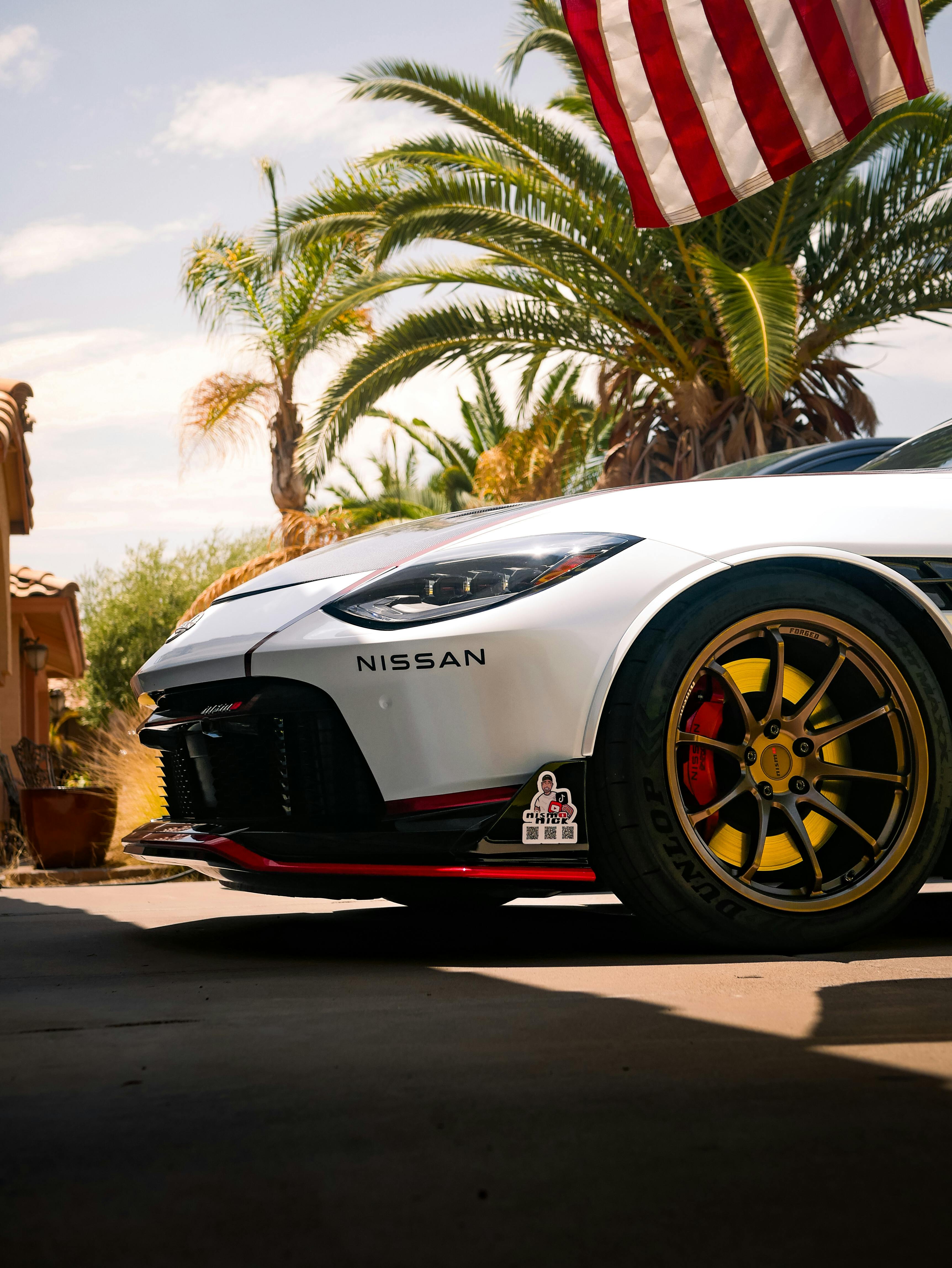 A white sports car with gold rims parked in front of an american flag ...