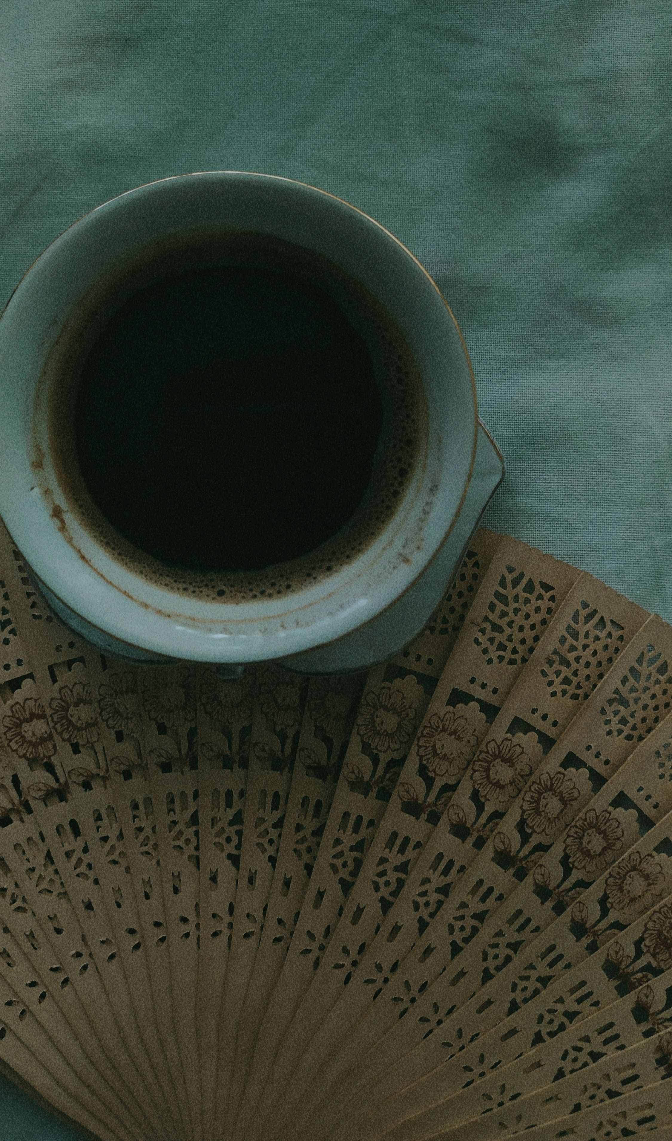 A cup of coffee and a fan on a table · Free Stock Photo
