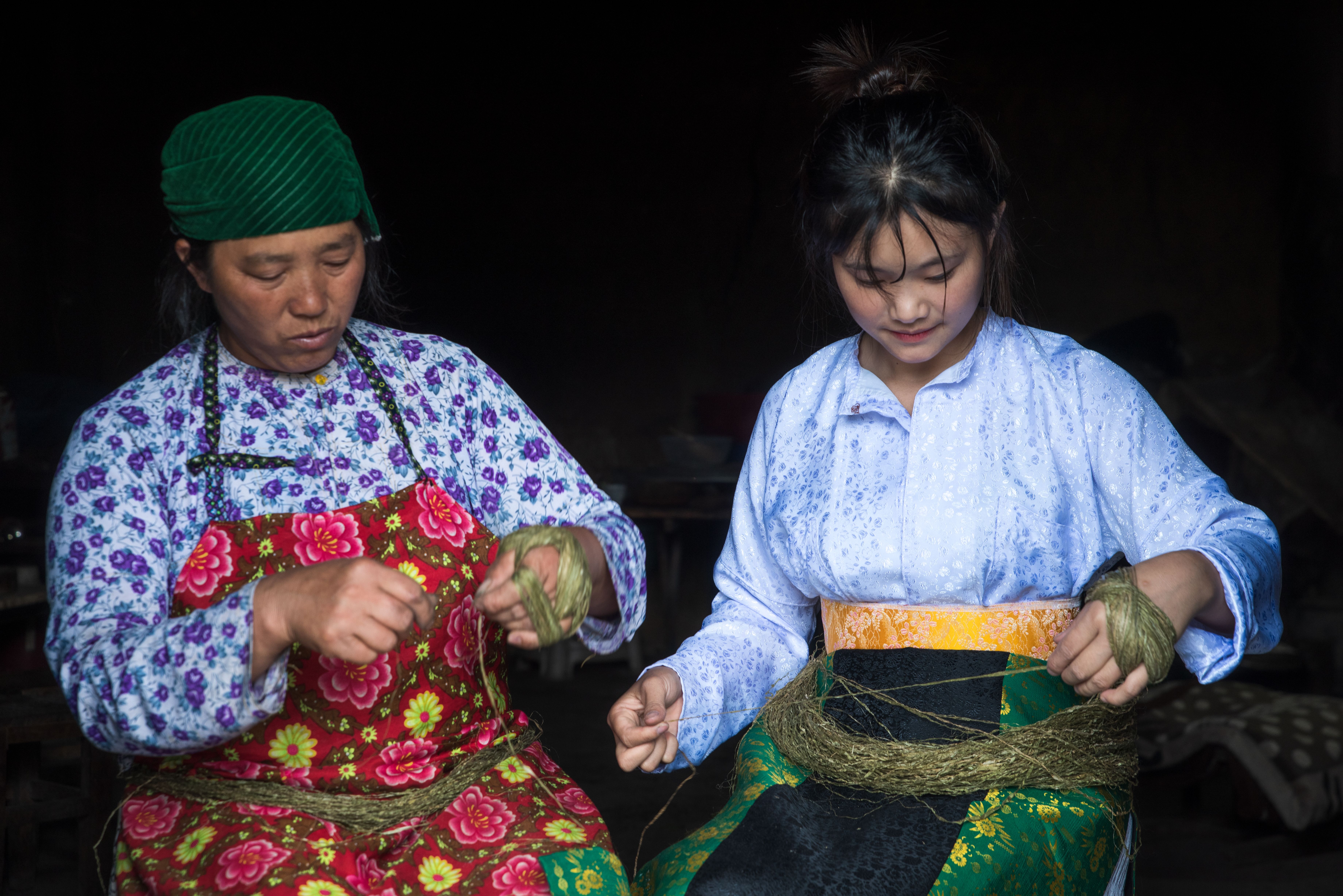 Two women in traditional clothing are working on a piece of material ...