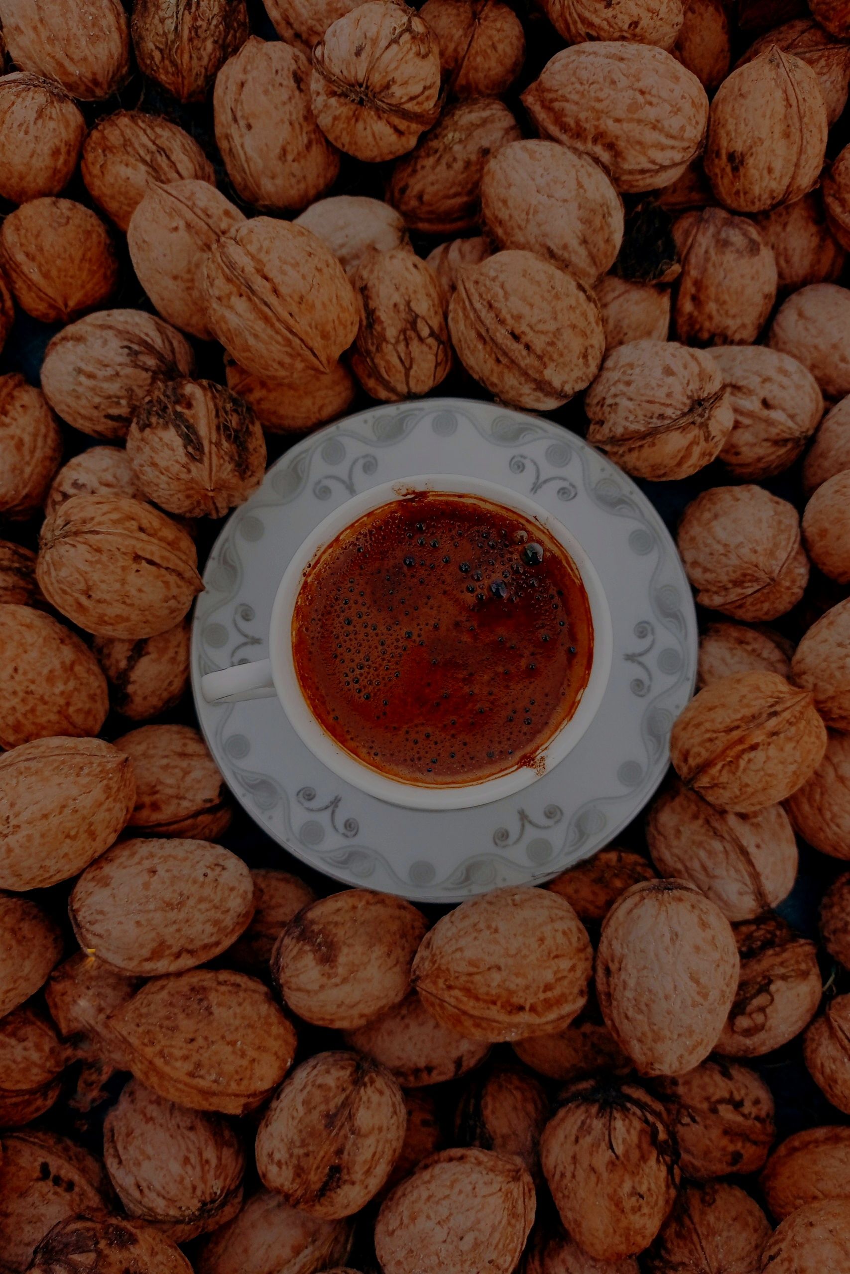 A cup of coffee sits on top of a pile of walnuts · Free Stock Photo