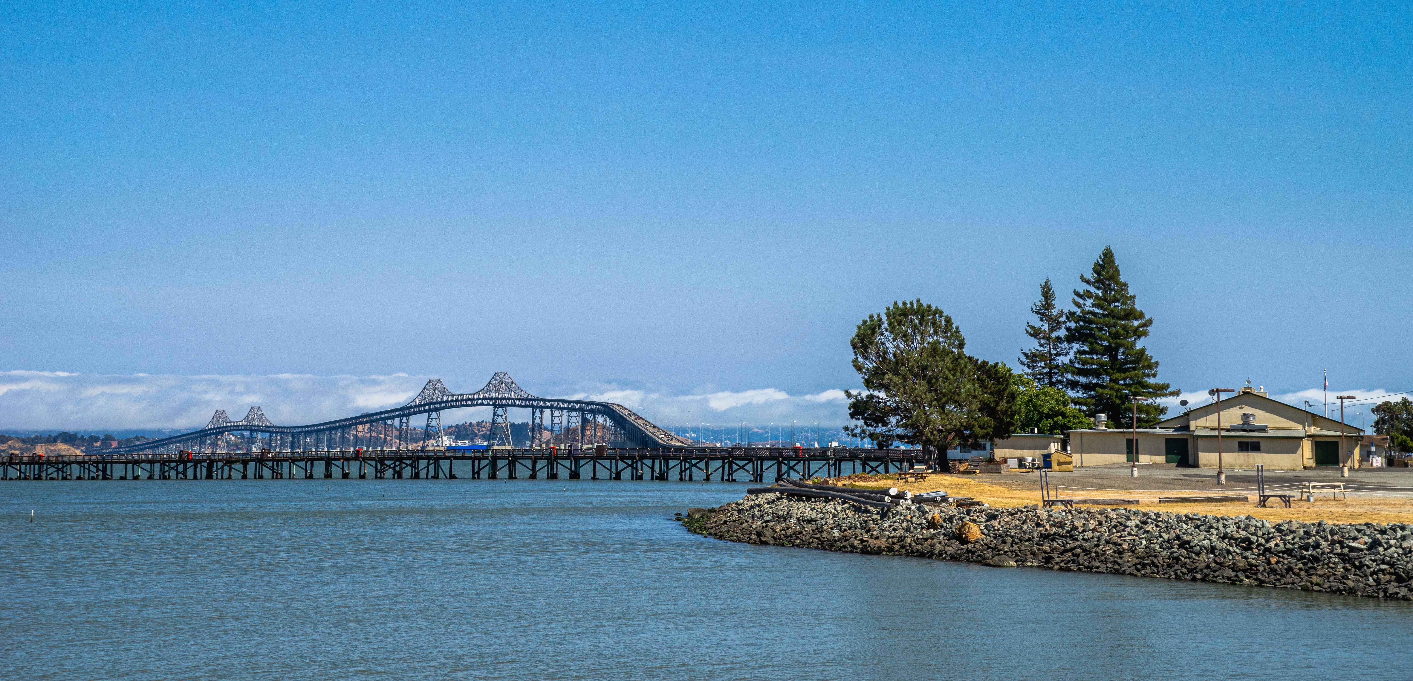 A view of a bridge over water with a beach and trees · Free Stock Photo