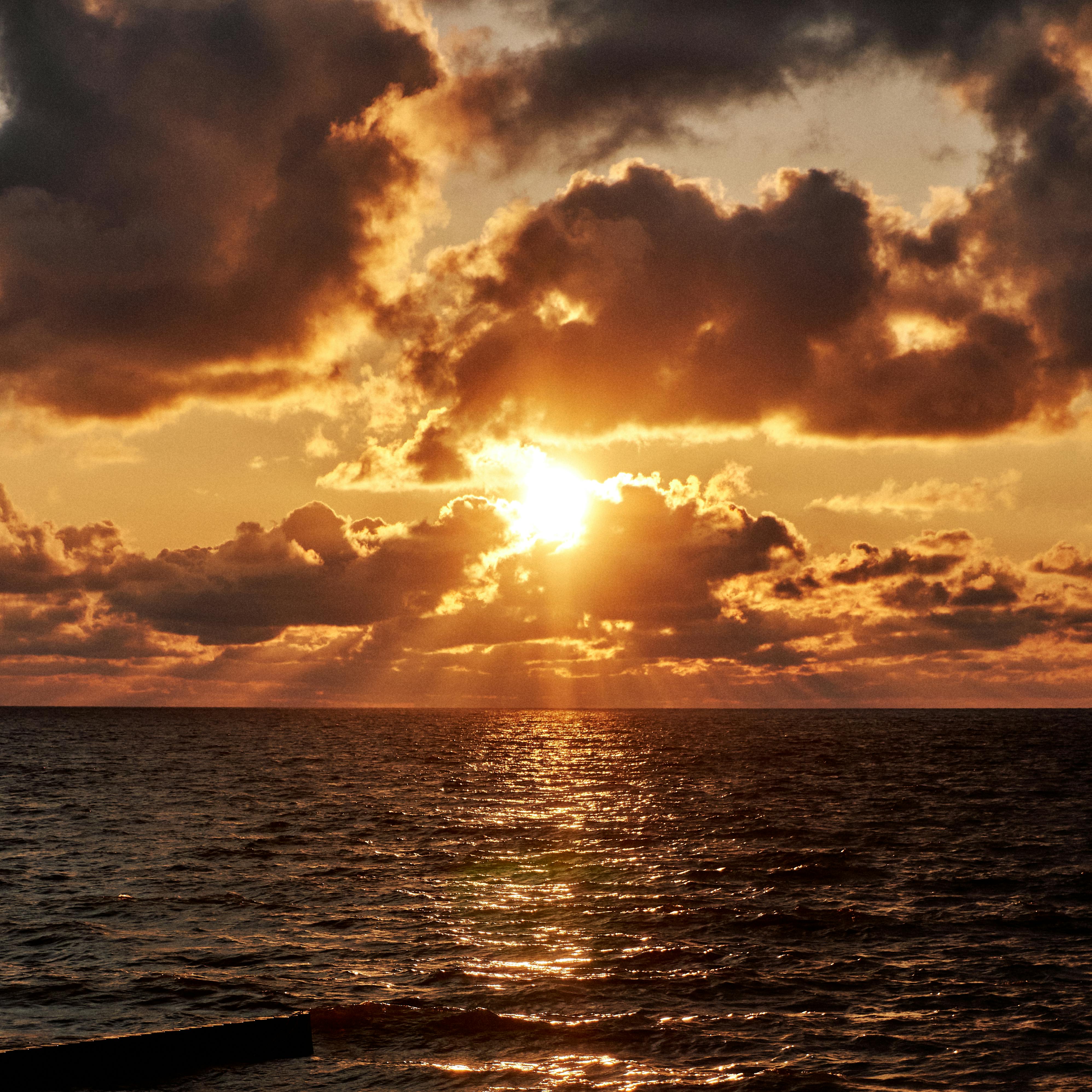 The sun is setting over the ocean with clouds · Free Stock Photo