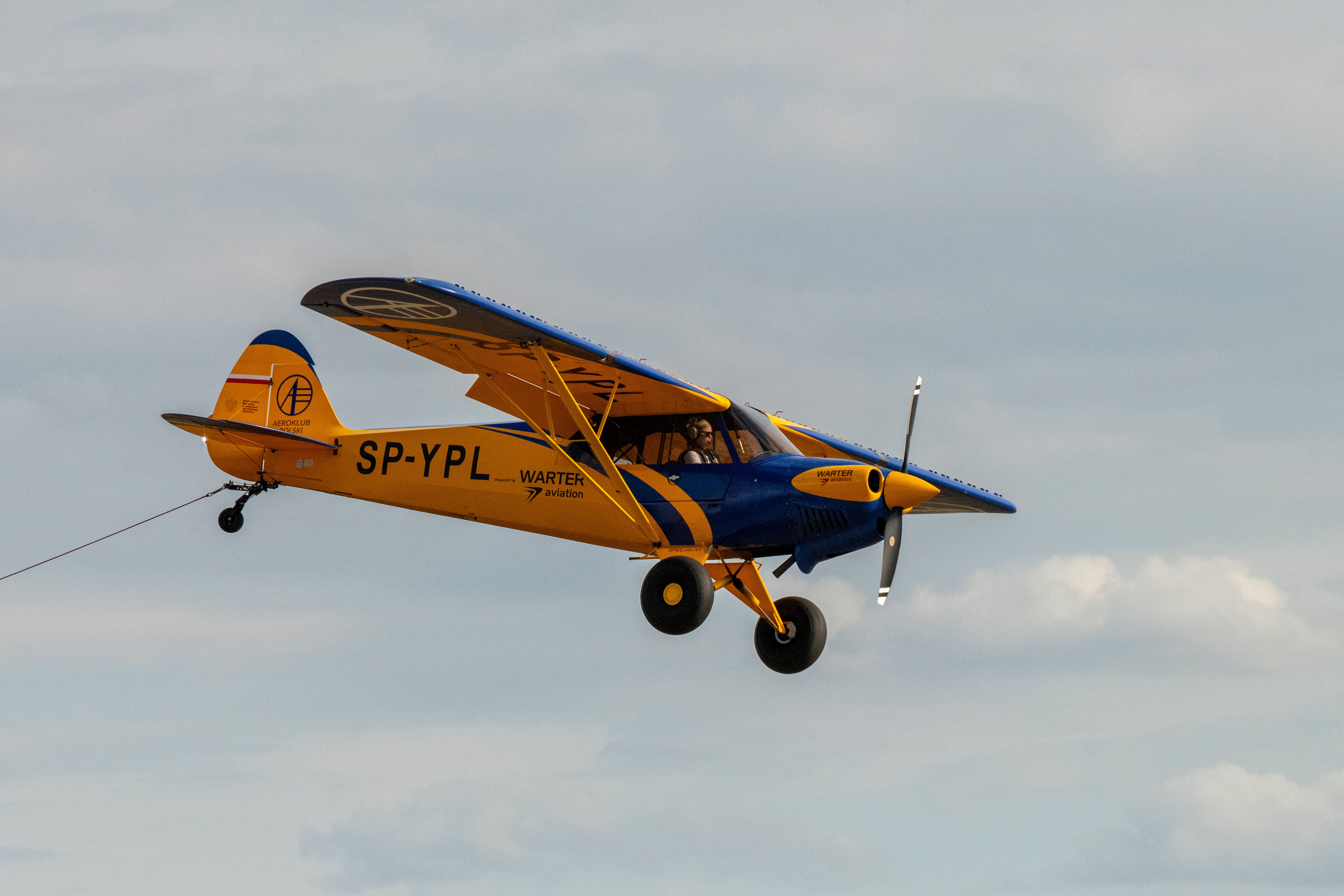 A small yellow and blue airplane flying in the sky · Free Stock Photo
