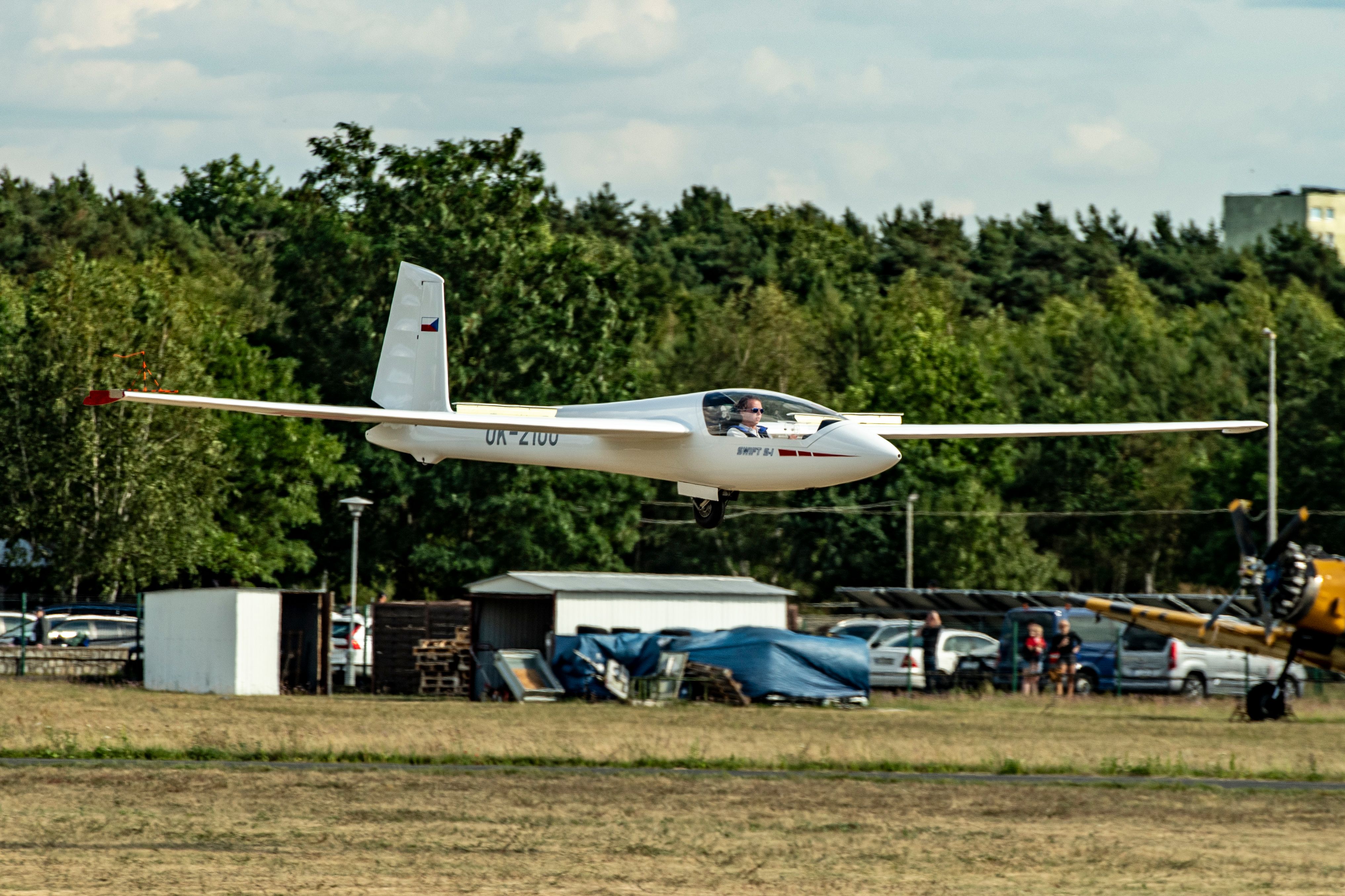 A small plane flying over a field with trees · Free Stock Photo