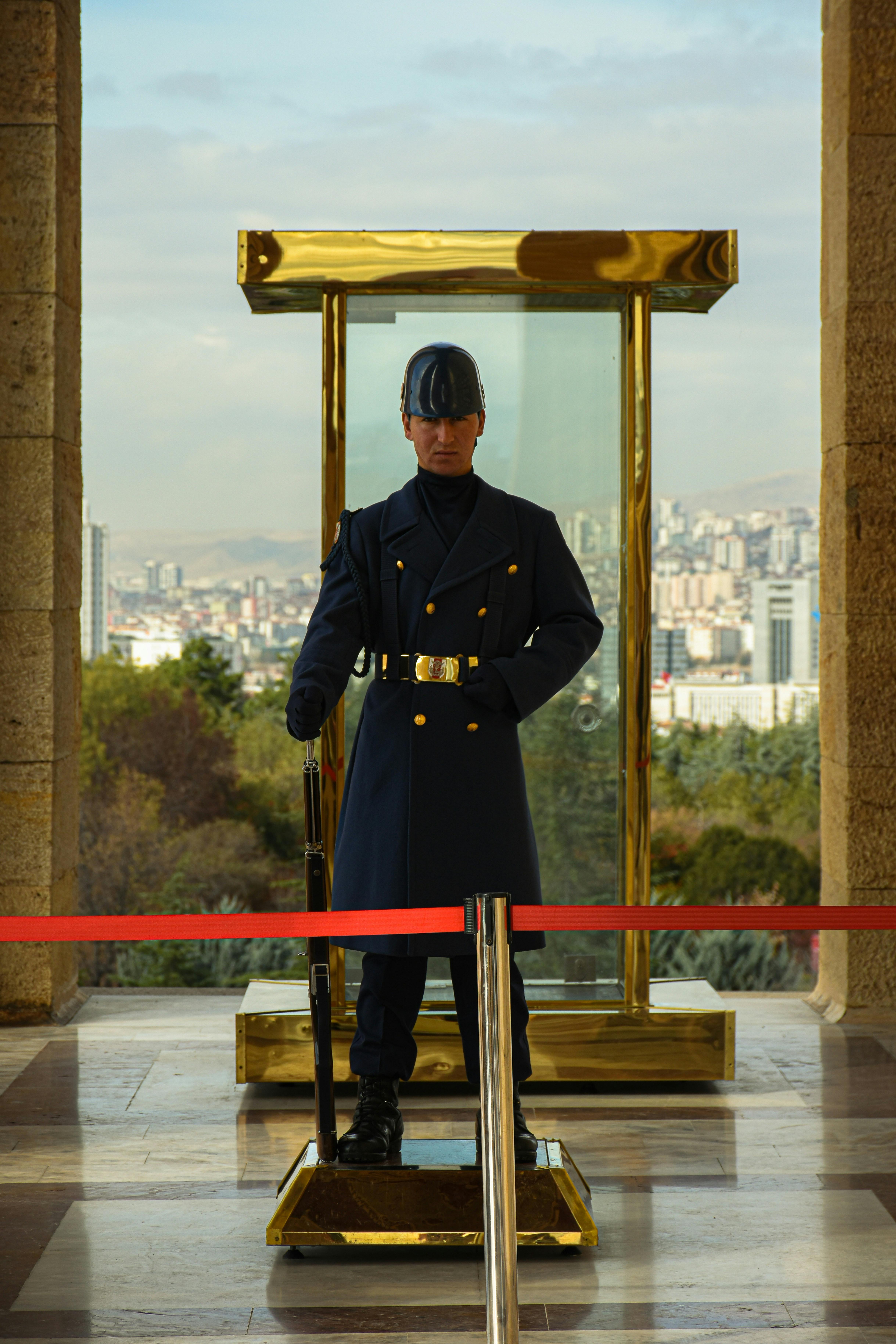 A man in uniform stands in front of a golden statue · Free Stock Photo