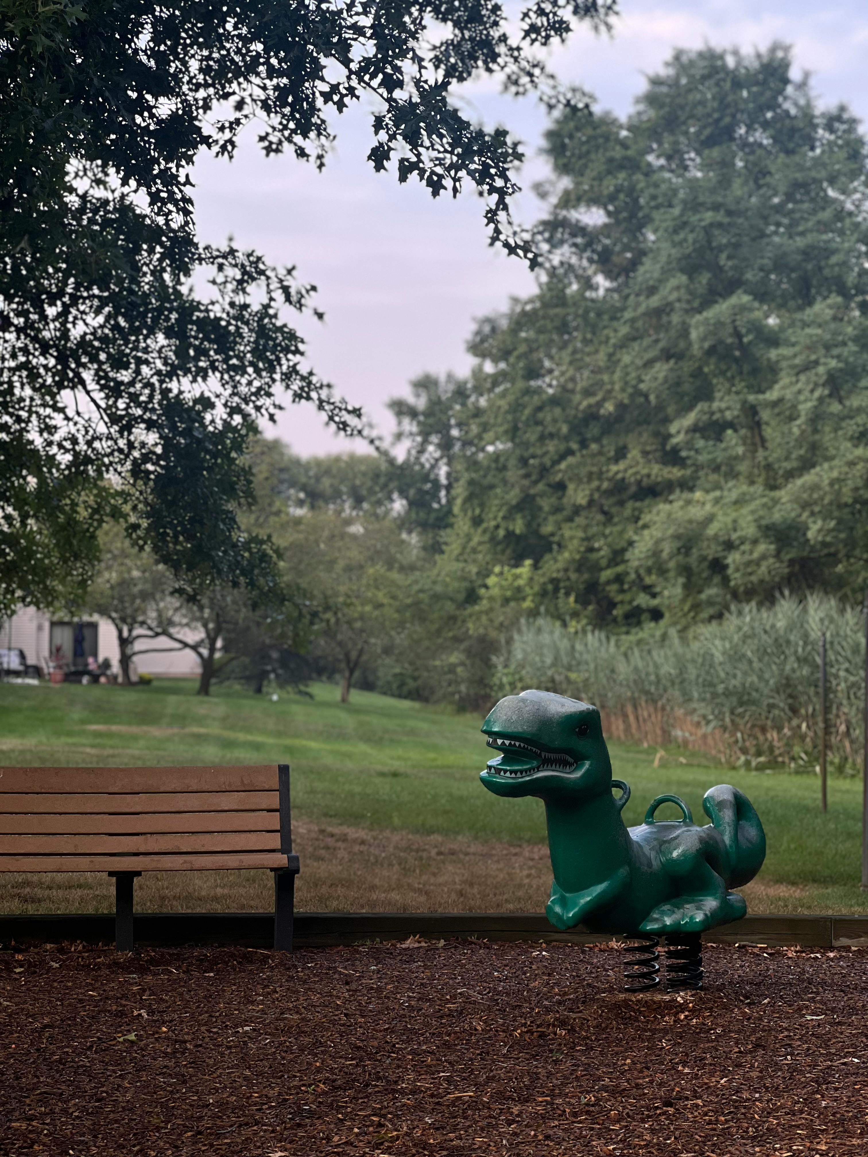 A green dinosaur toy sitting on a bench in a park · Free Stock Photo