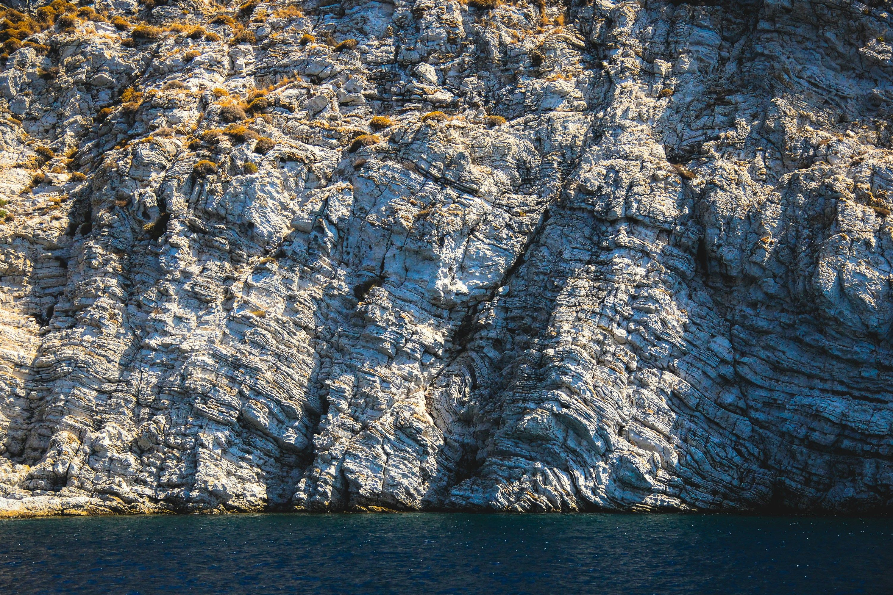 A boat is sailing by a cliff with a blue sky · Free Stock Photo