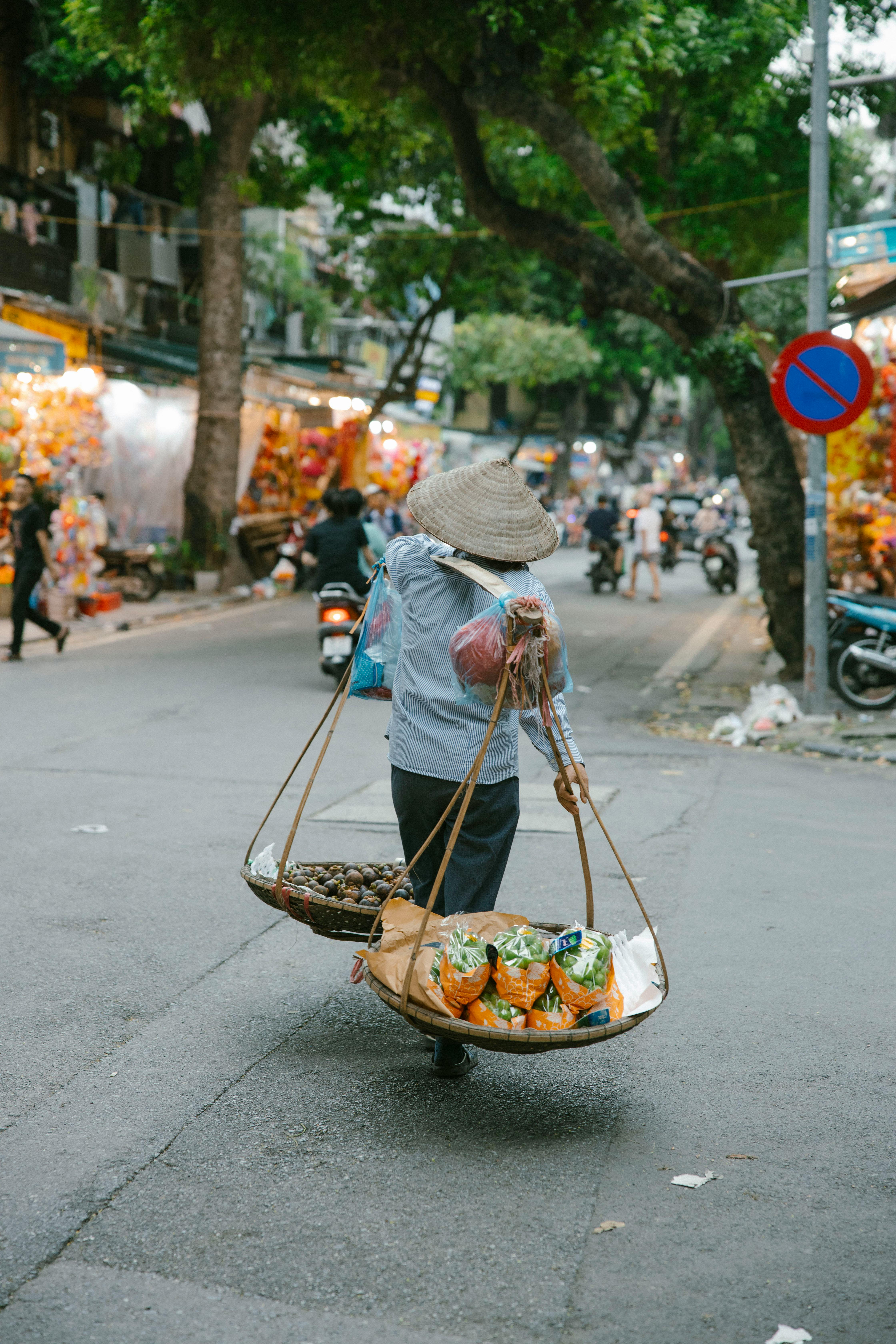 A woman carrying baskets of fruit on the street · Free Stock Photo