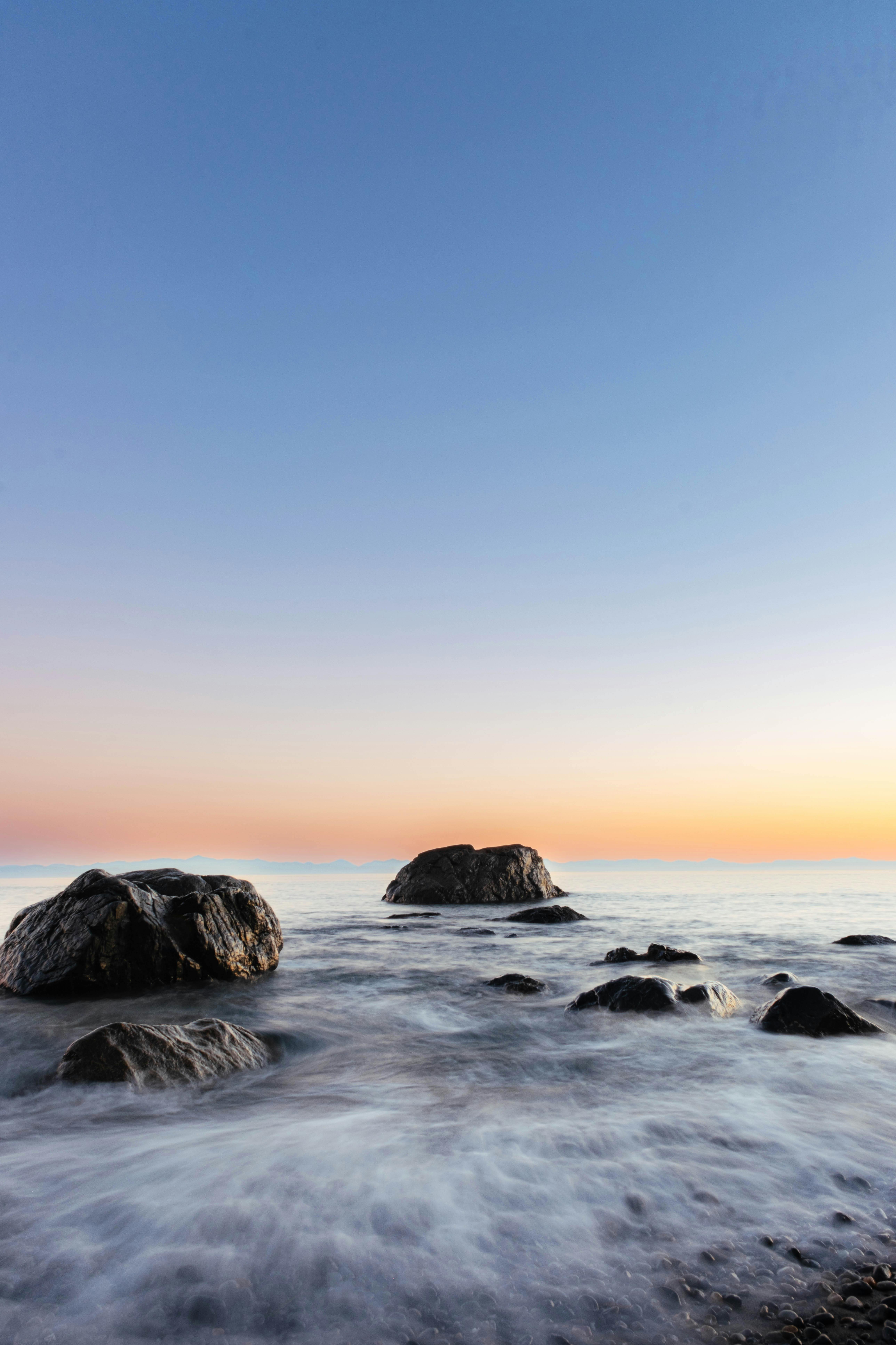 A sunset over the ocean with rocks and water · Free Stock Photo