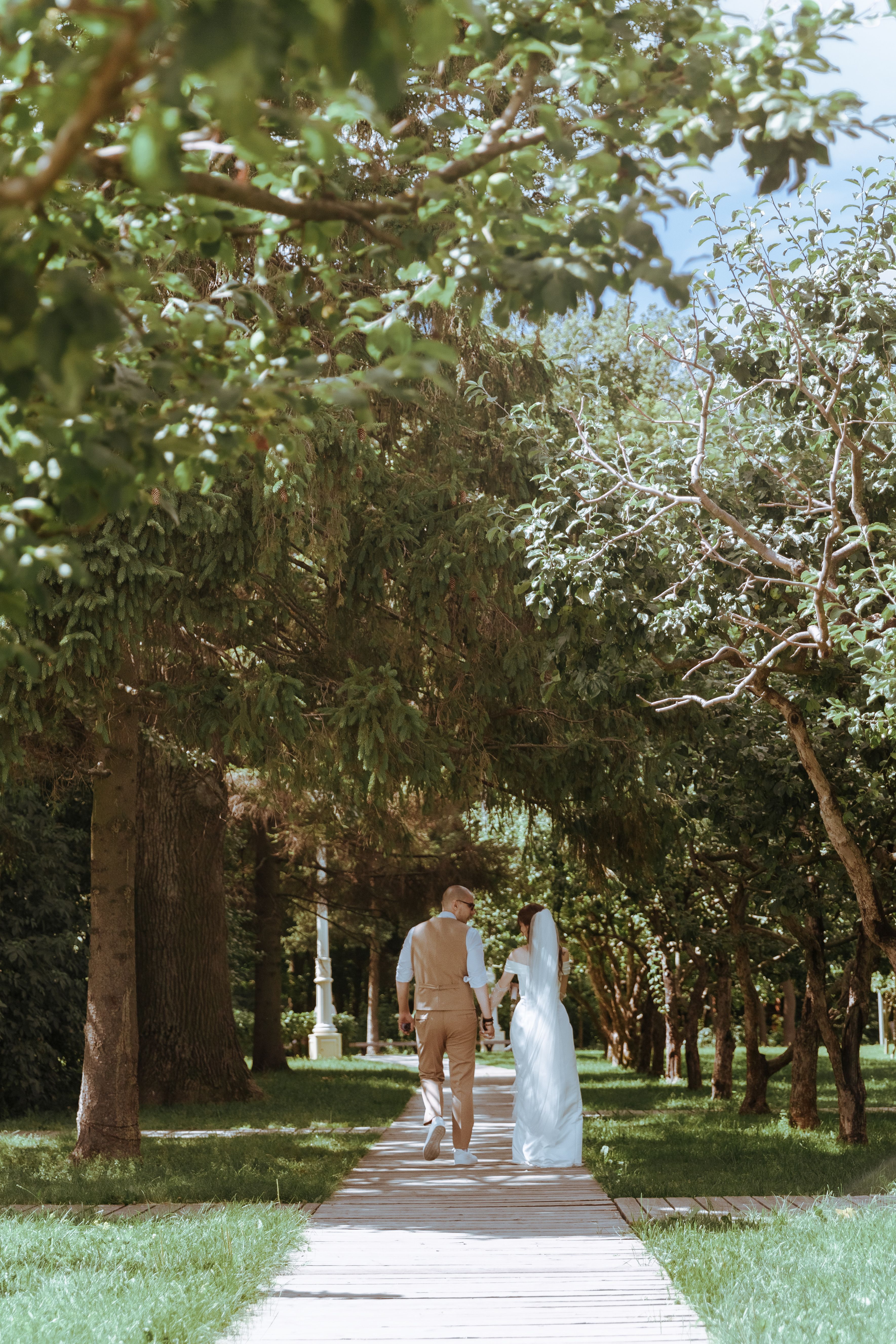 A bride and groom walking down a path in the park · Free Stock Photo