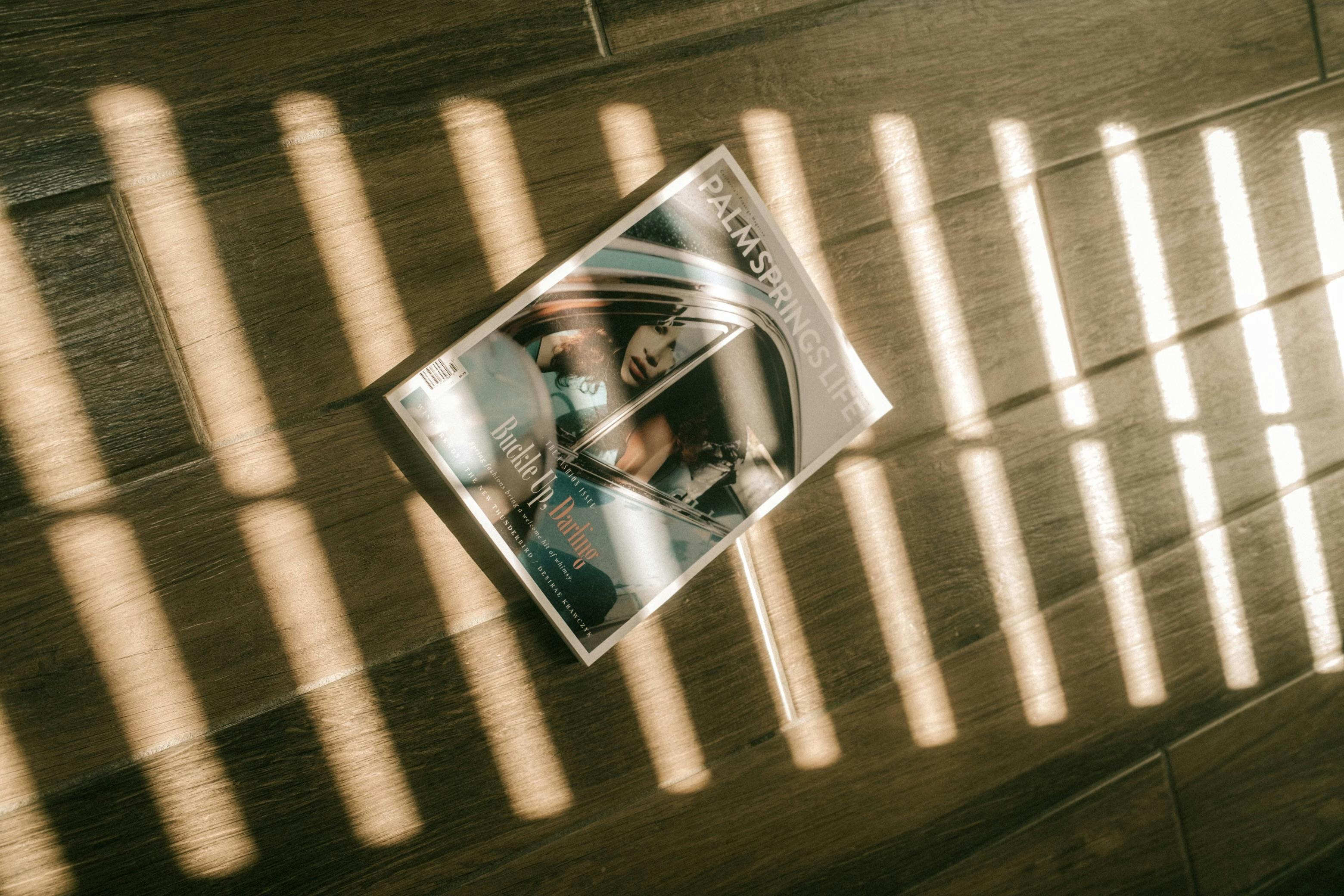 A magazine laying on the floor with sunlight shining through the window ...