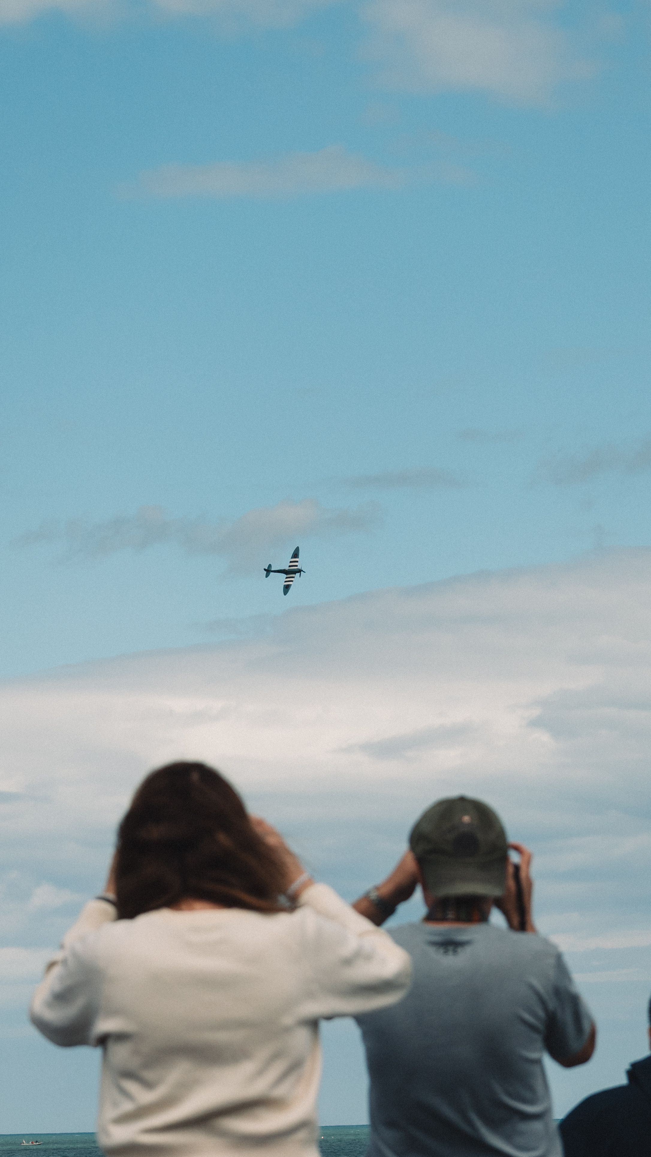 A group of people watching a plane fly over the ocean · Free Stock Photo