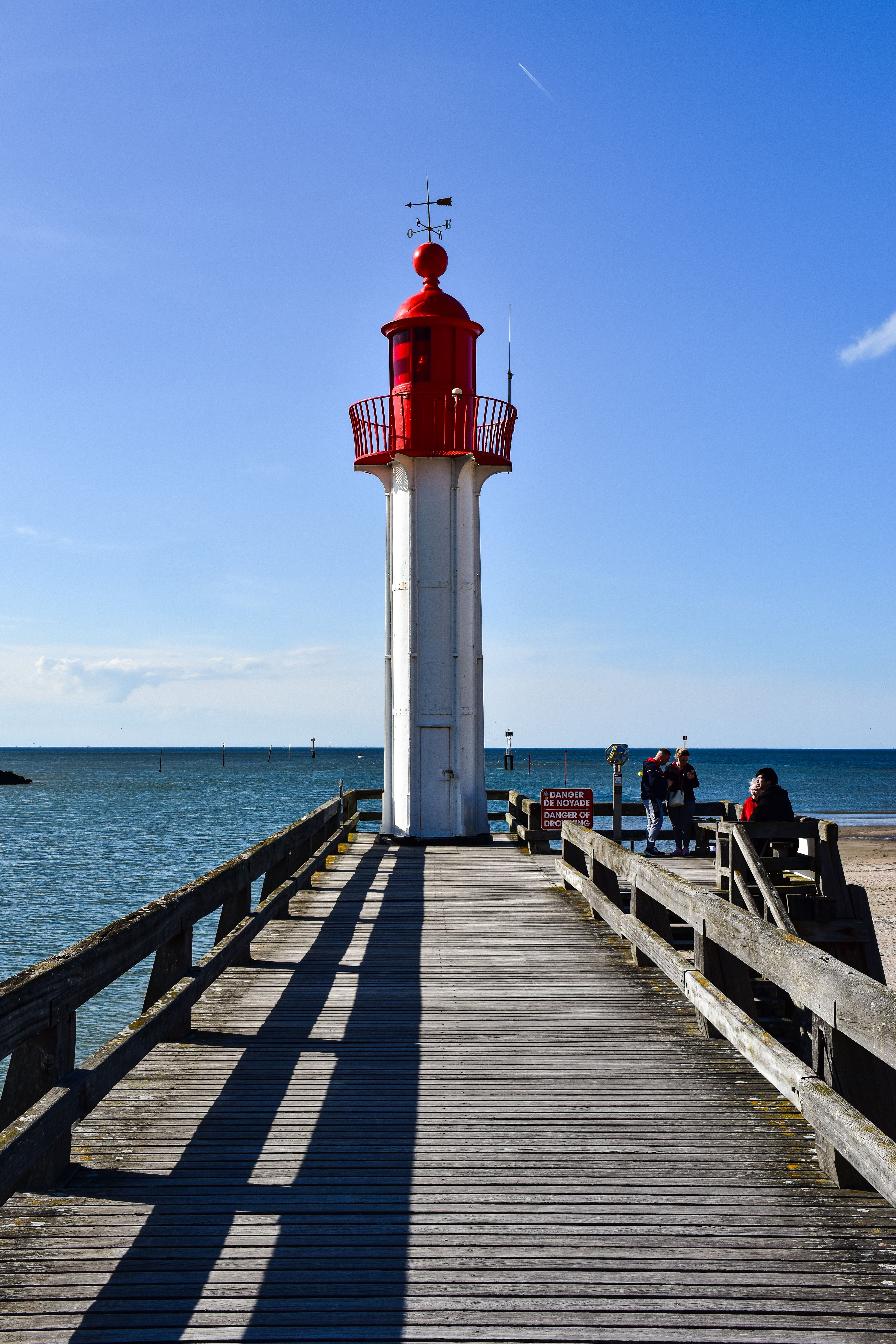 A red lighthouse on a pier with a wooden walkway · Free Stock Photo