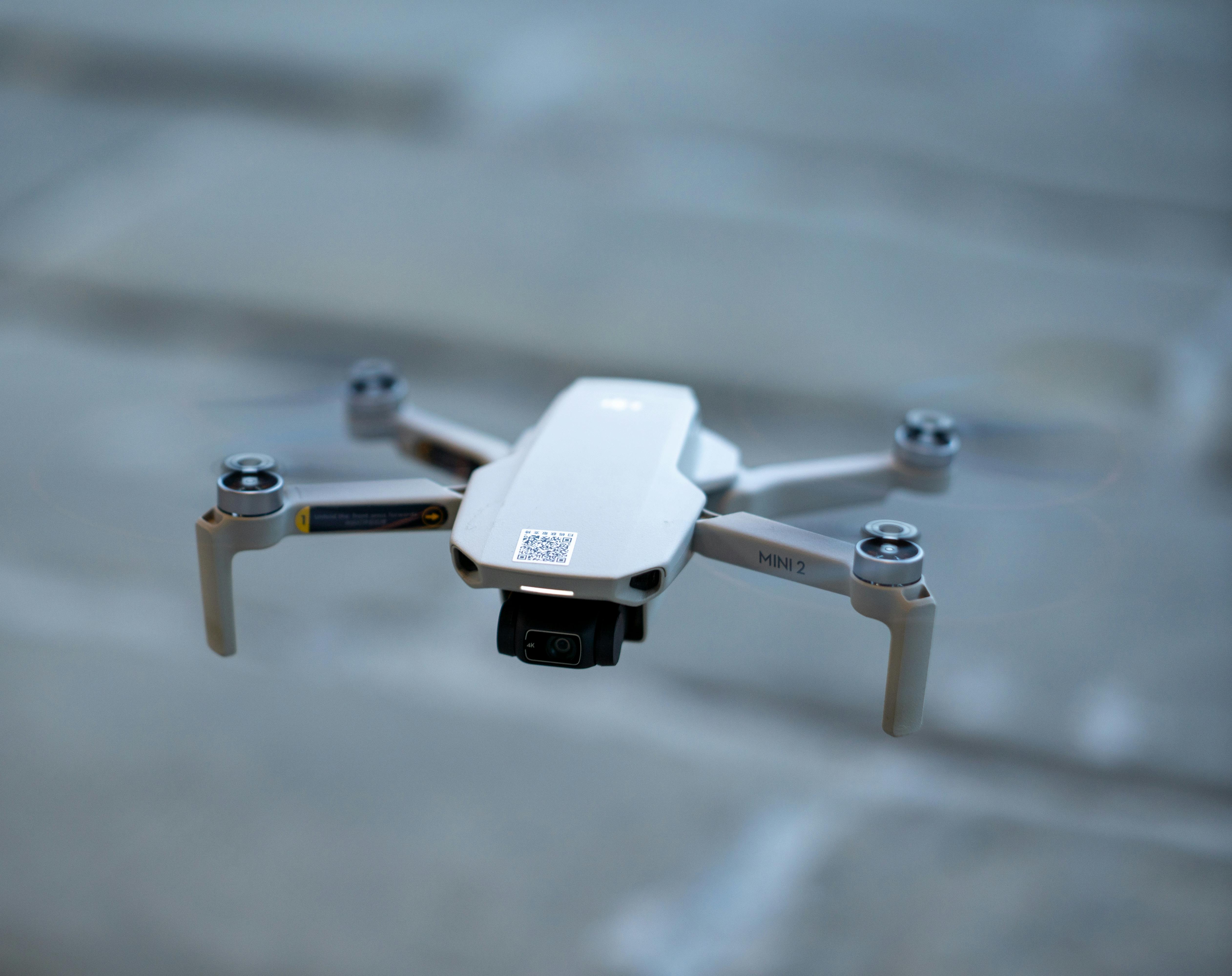 A small white drone flying over a brick wall · Free Stock Photo