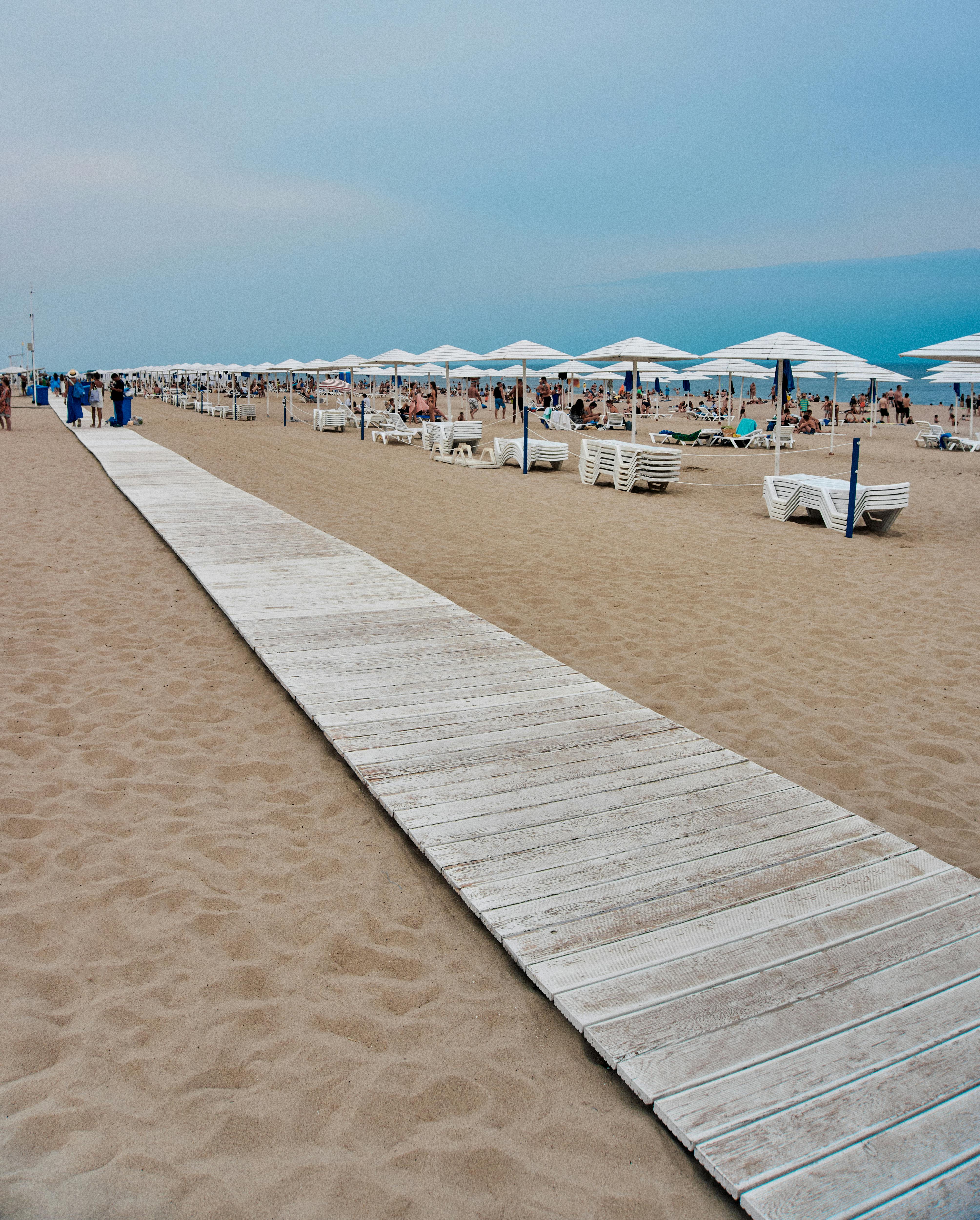 A wooden walkway leading to the beach with umbrellas · Free Stock Photo