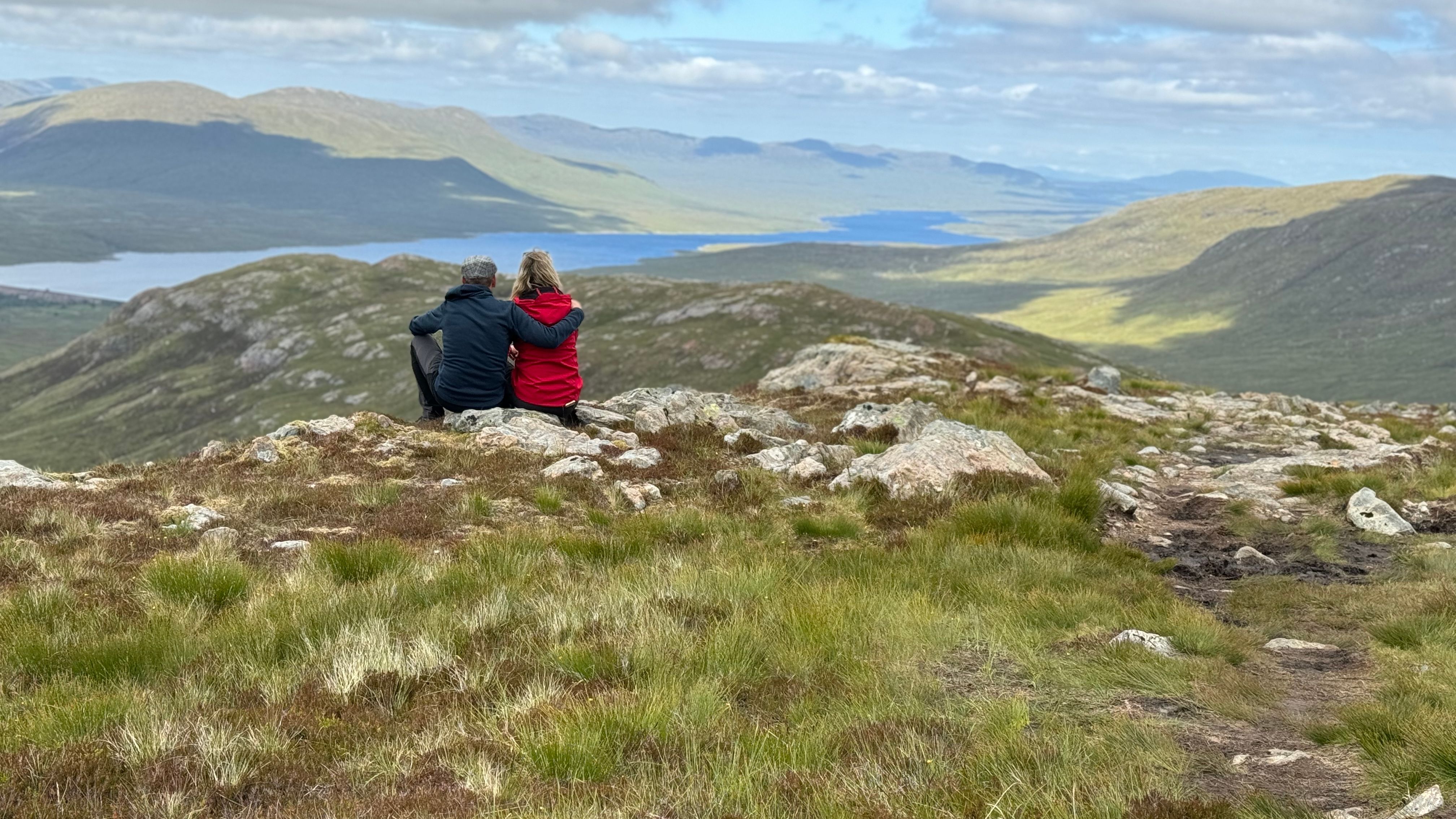 Two people sitting on a hill overlooking a lake · Free Stock Photo