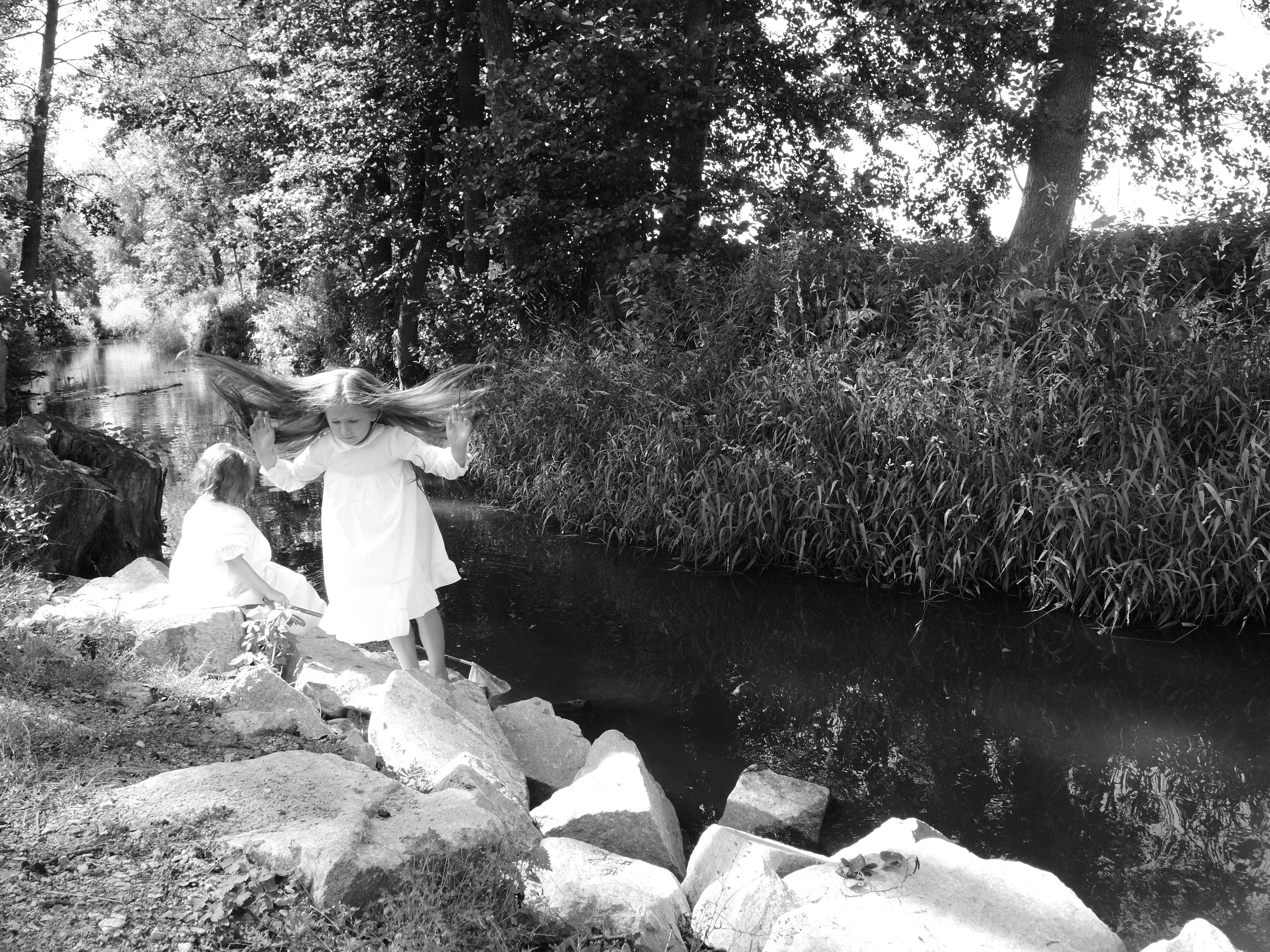 Two children are standing on rocks by a stream · Free Stock Photo