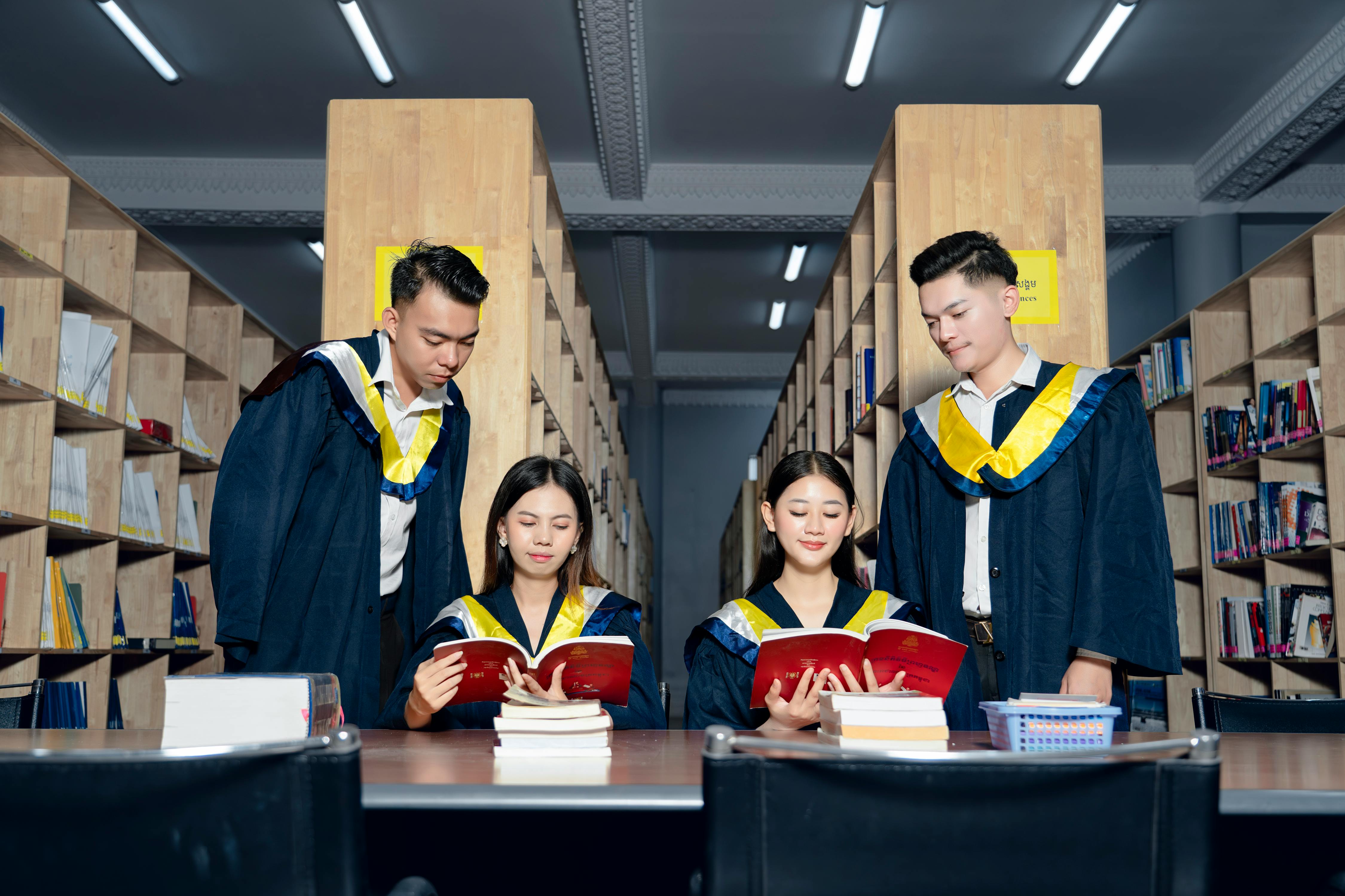Four students in graduation robes are sitting at a table · Free Stock Photo