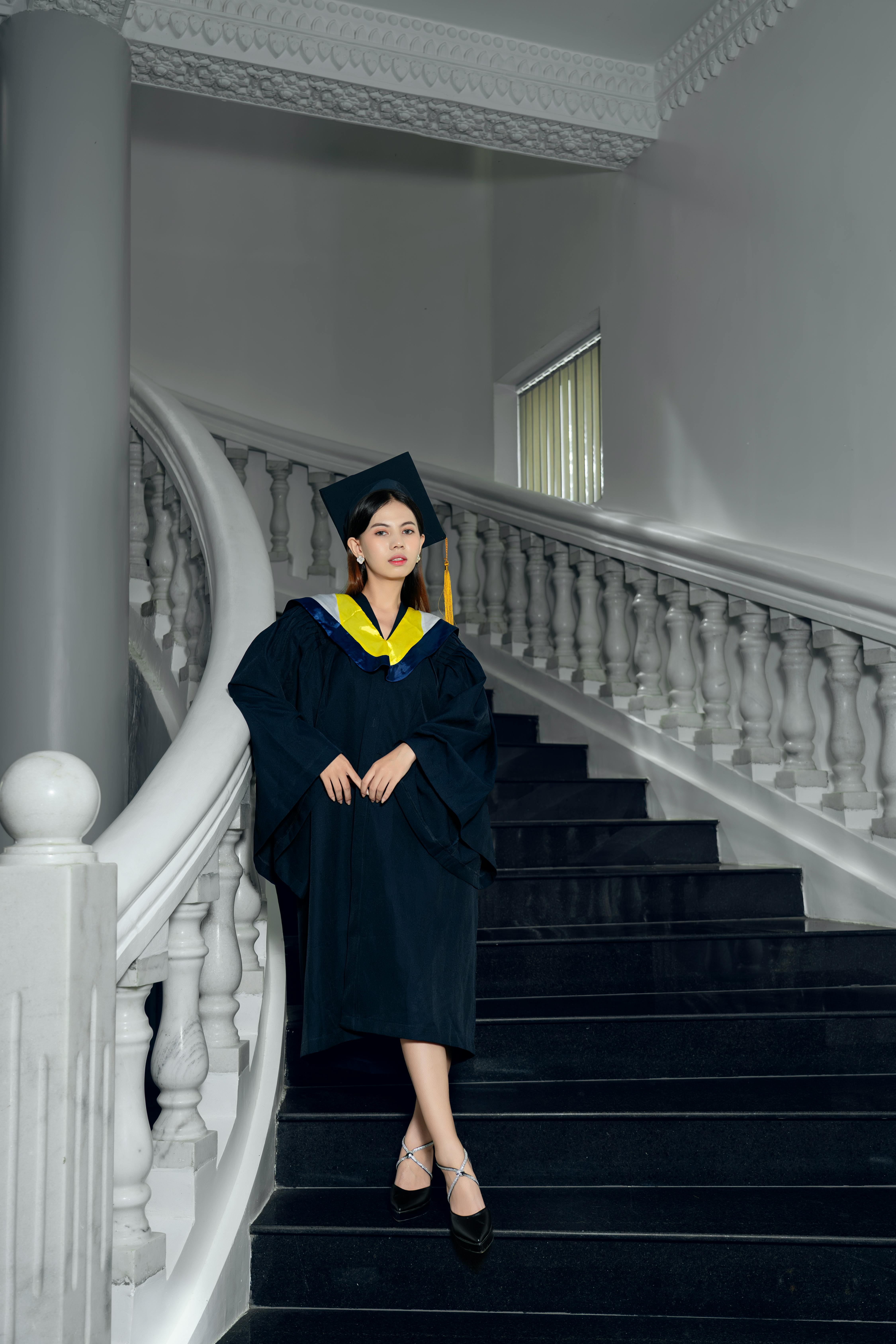 A woman in a graduation gown posing on the stairs · Free Stock Photo