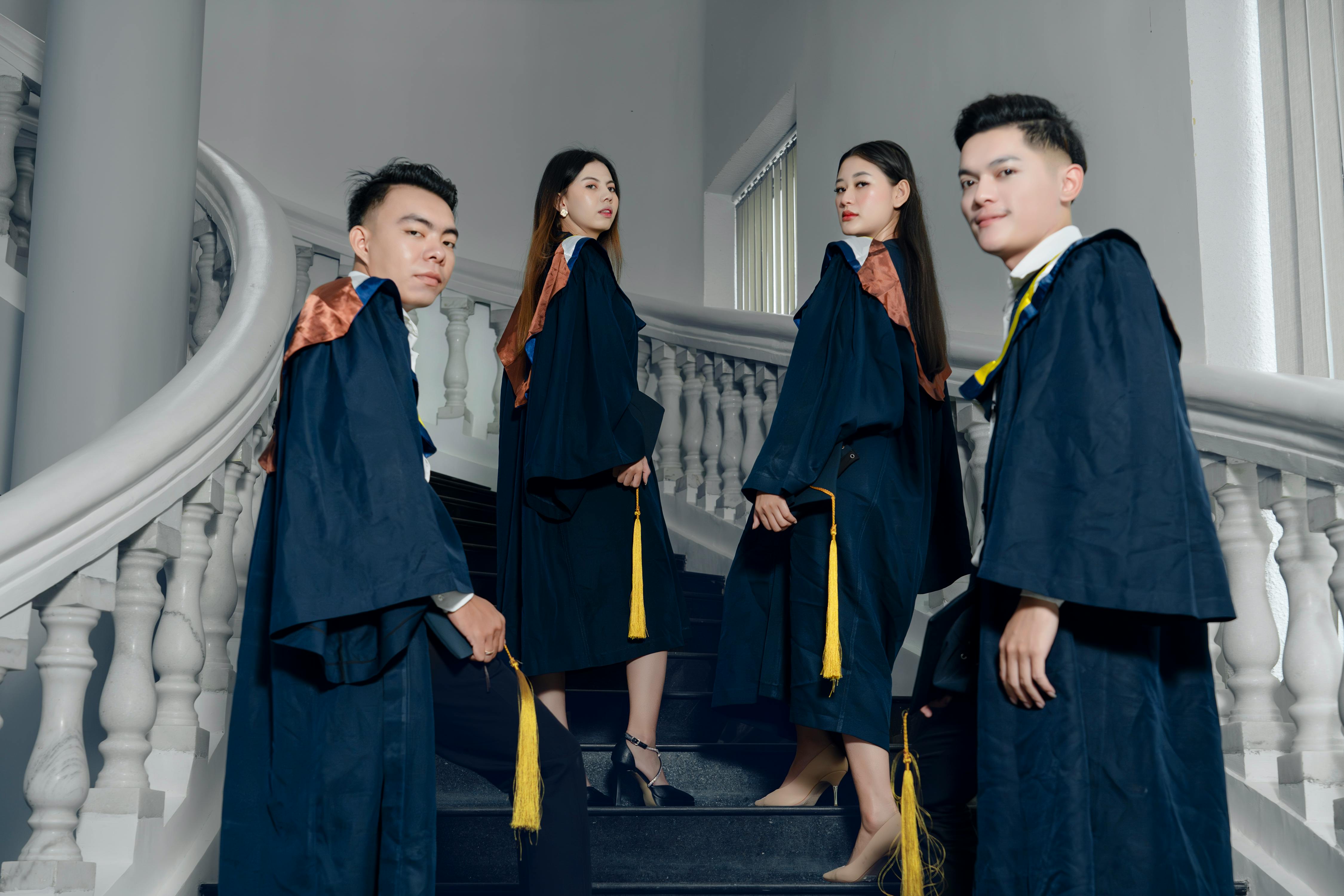 Four graduates in graduation gowns standing on stairs · Free Stock Photo