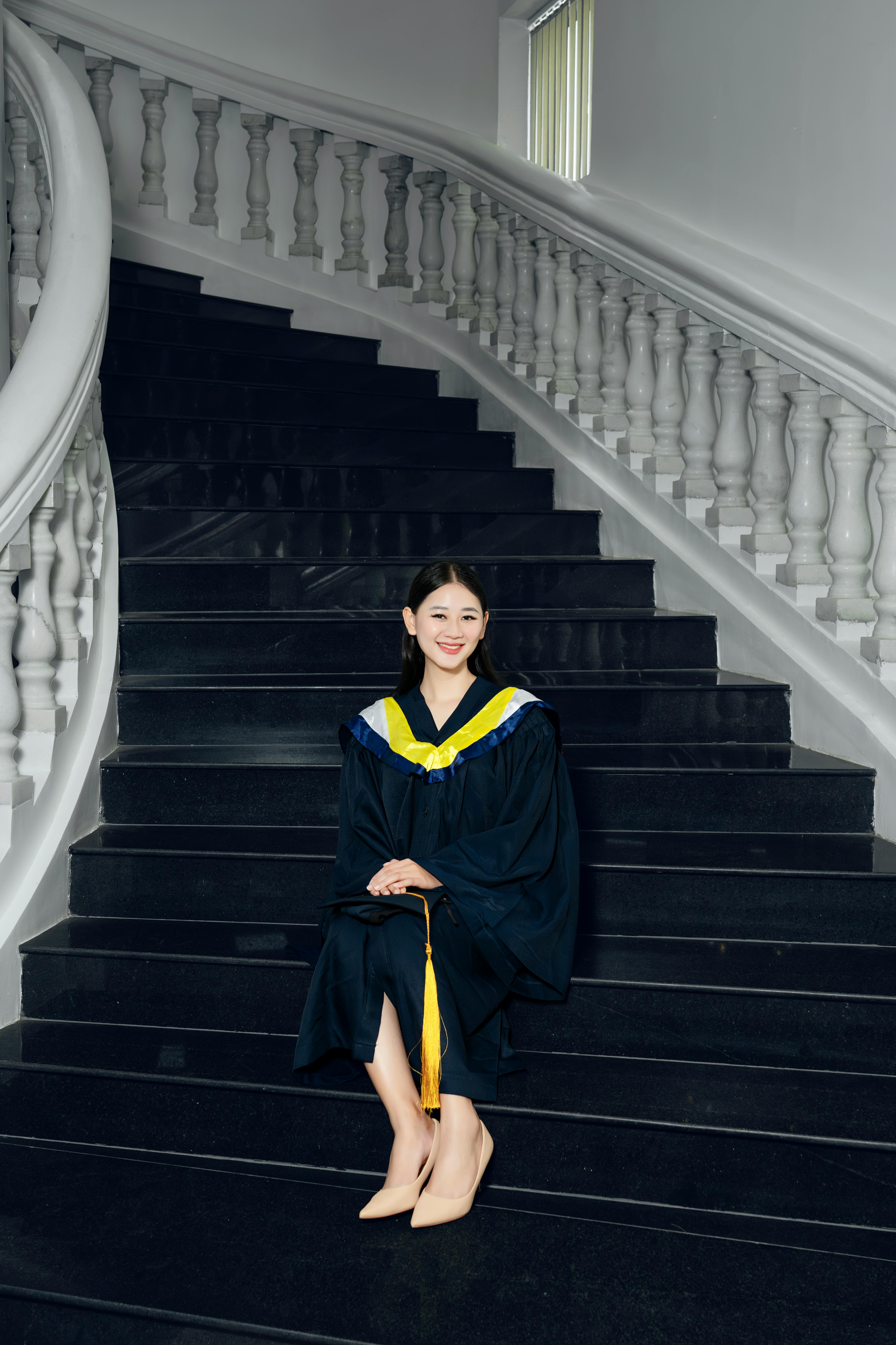 A woman in a graduation gown sitting on the stairs · Free Stock Photo