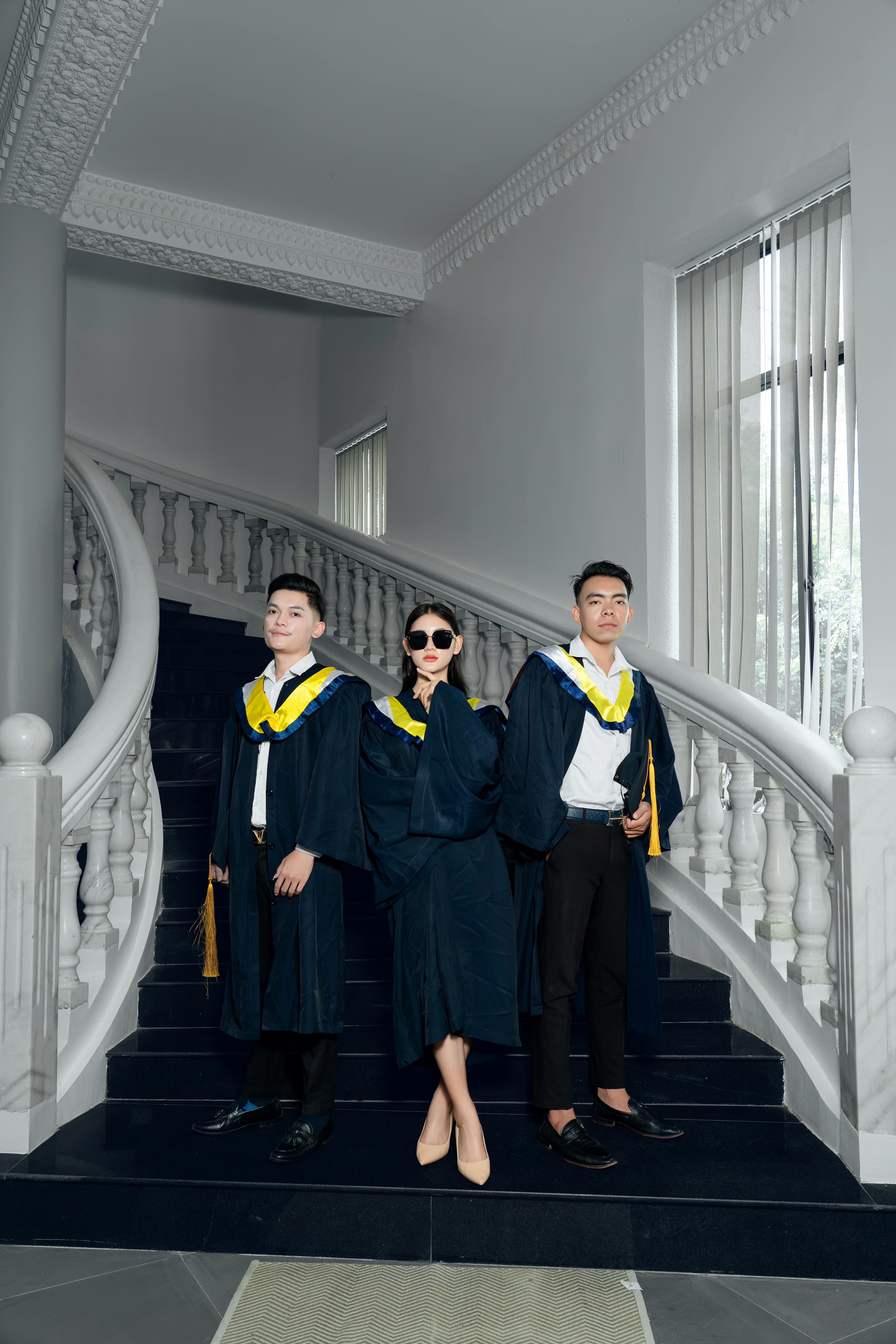 Three people in graduation gowns standing on a staircase · Free Stock Photo