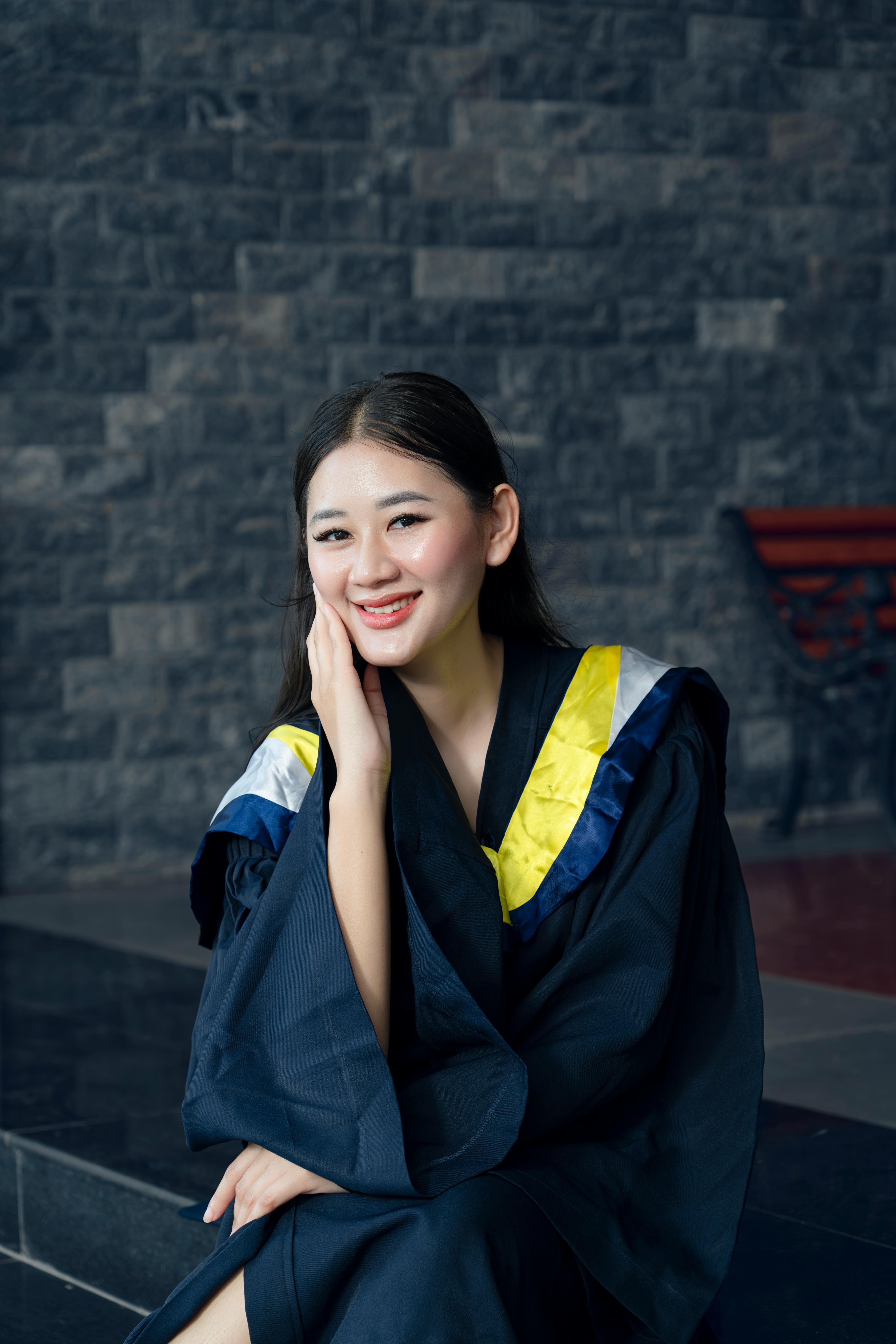 A woman in a graduation gown sitting on a bench · Free Stock Photo