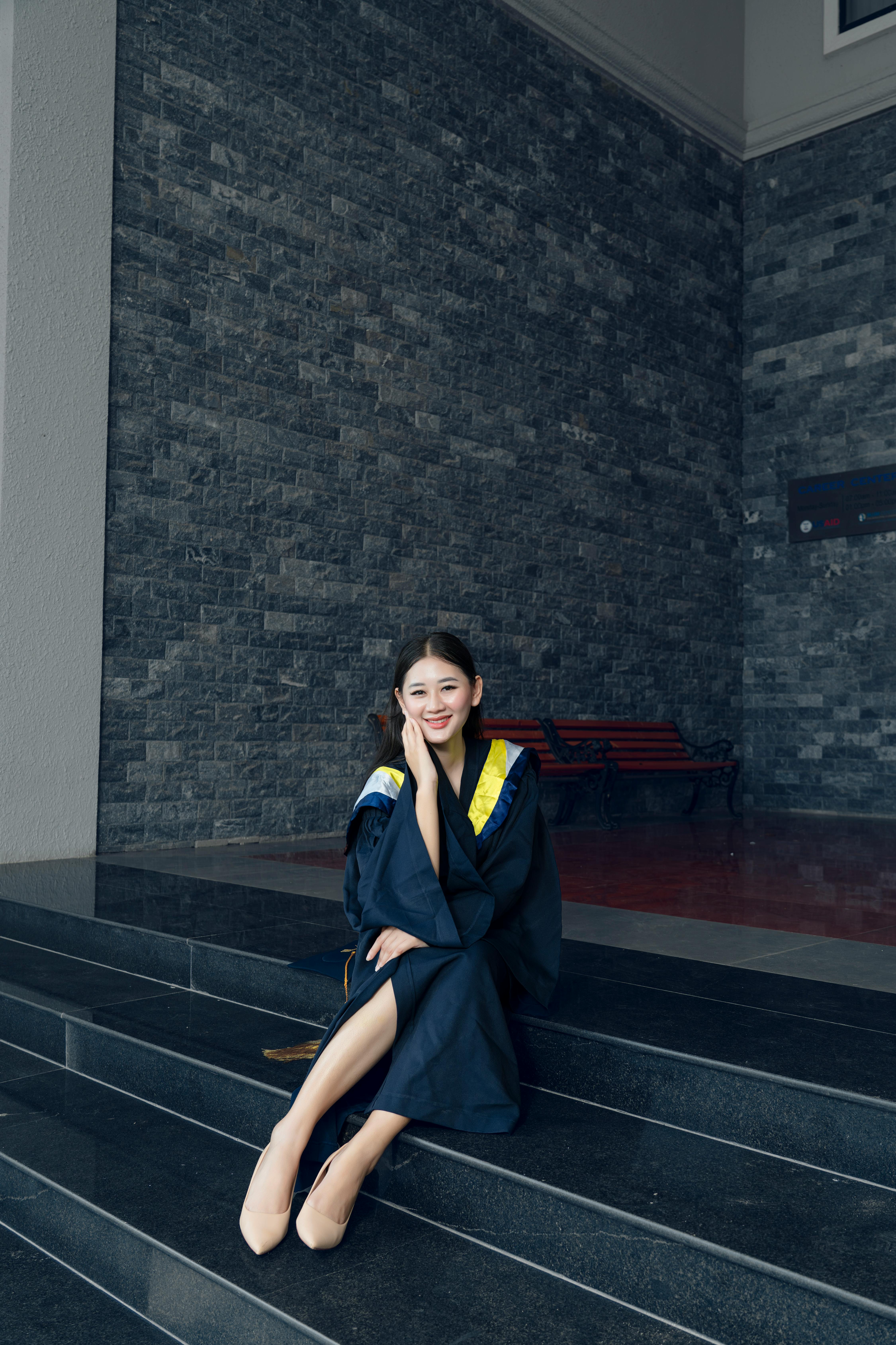 A woman in a graduation gown sitting on some steps · Free Stock Photo