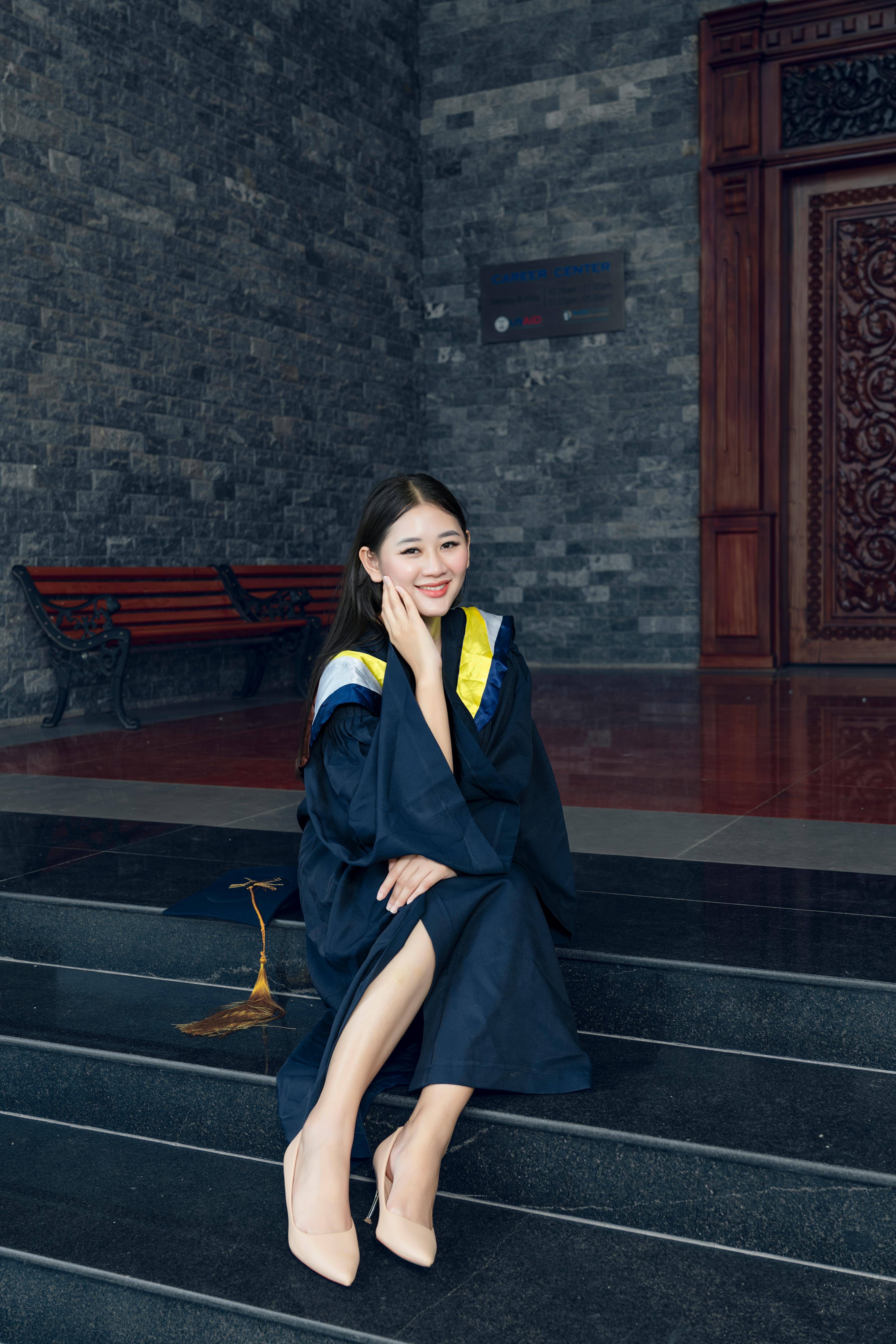A woman in a graduation gown sitting on some steps · Free Stock Photo