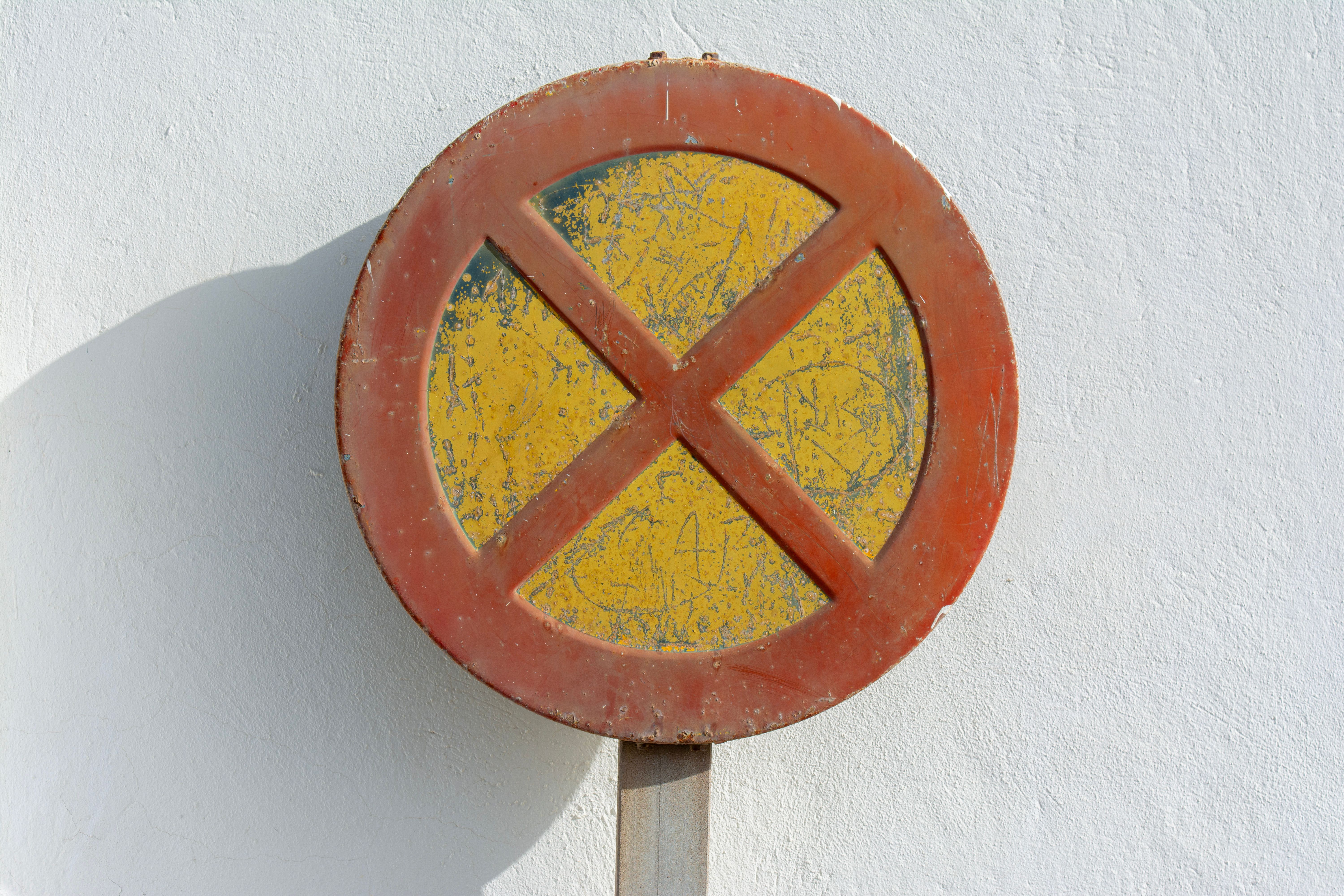 A yellow and red traffic sign on a white wall · Free Stock Photo
