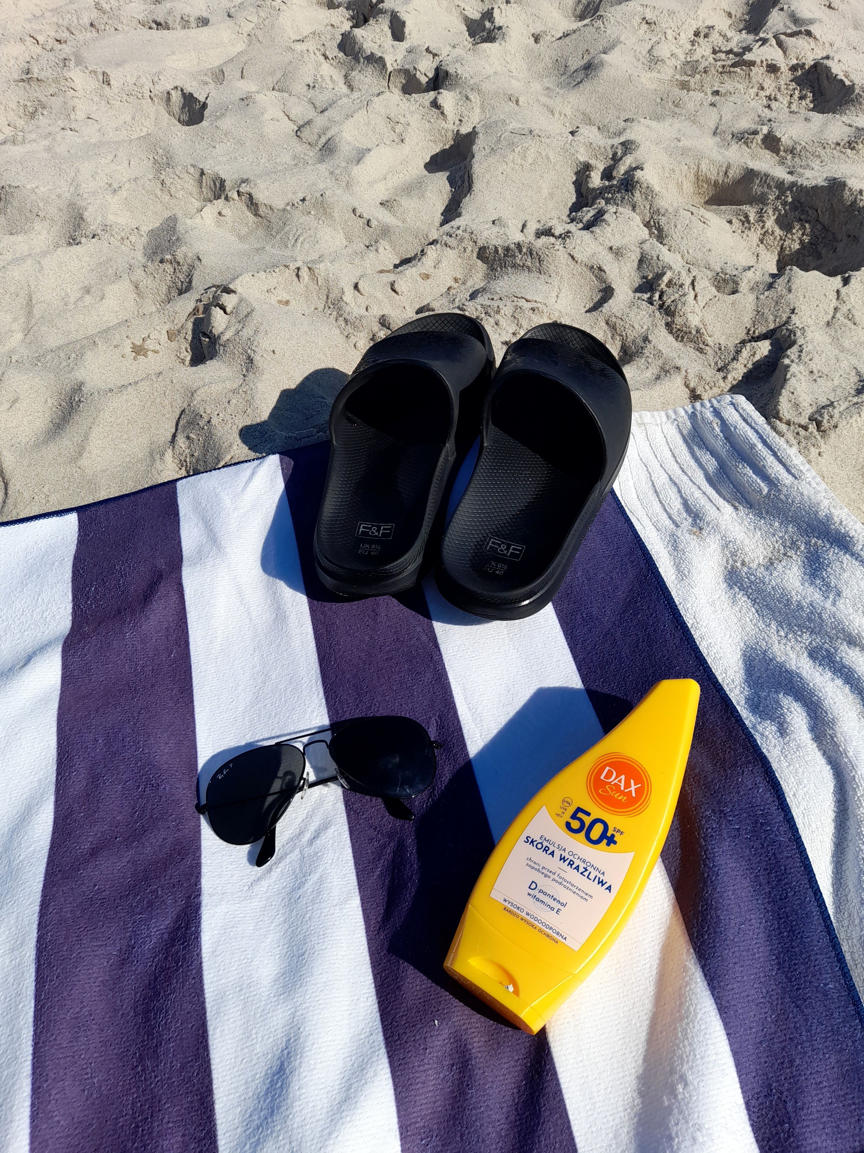 Sunscreen, sunglasses and a towel on the beach · Free Stock Photo