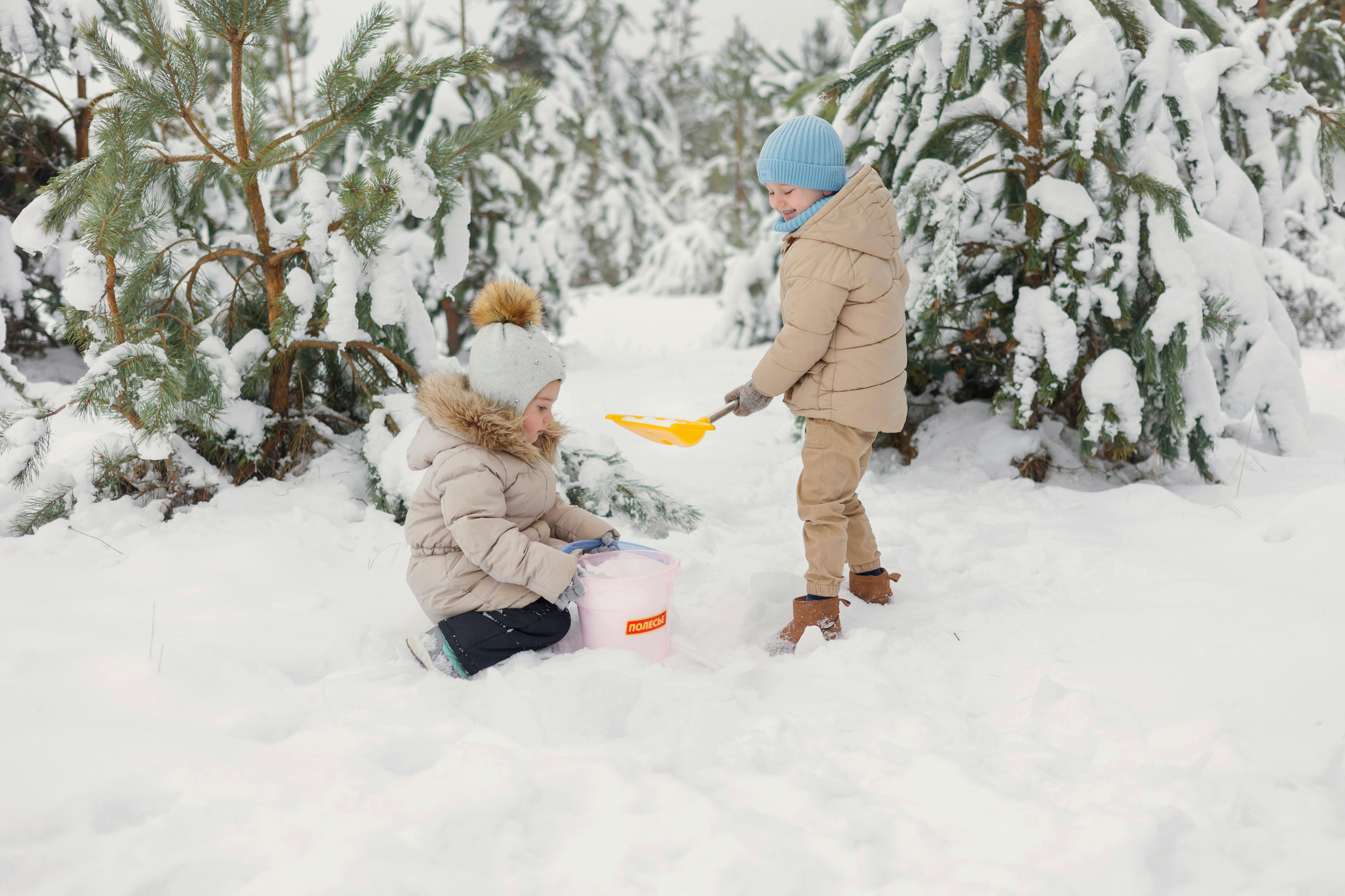 Two children playing in the snow with a bucket · Free Stock Photo