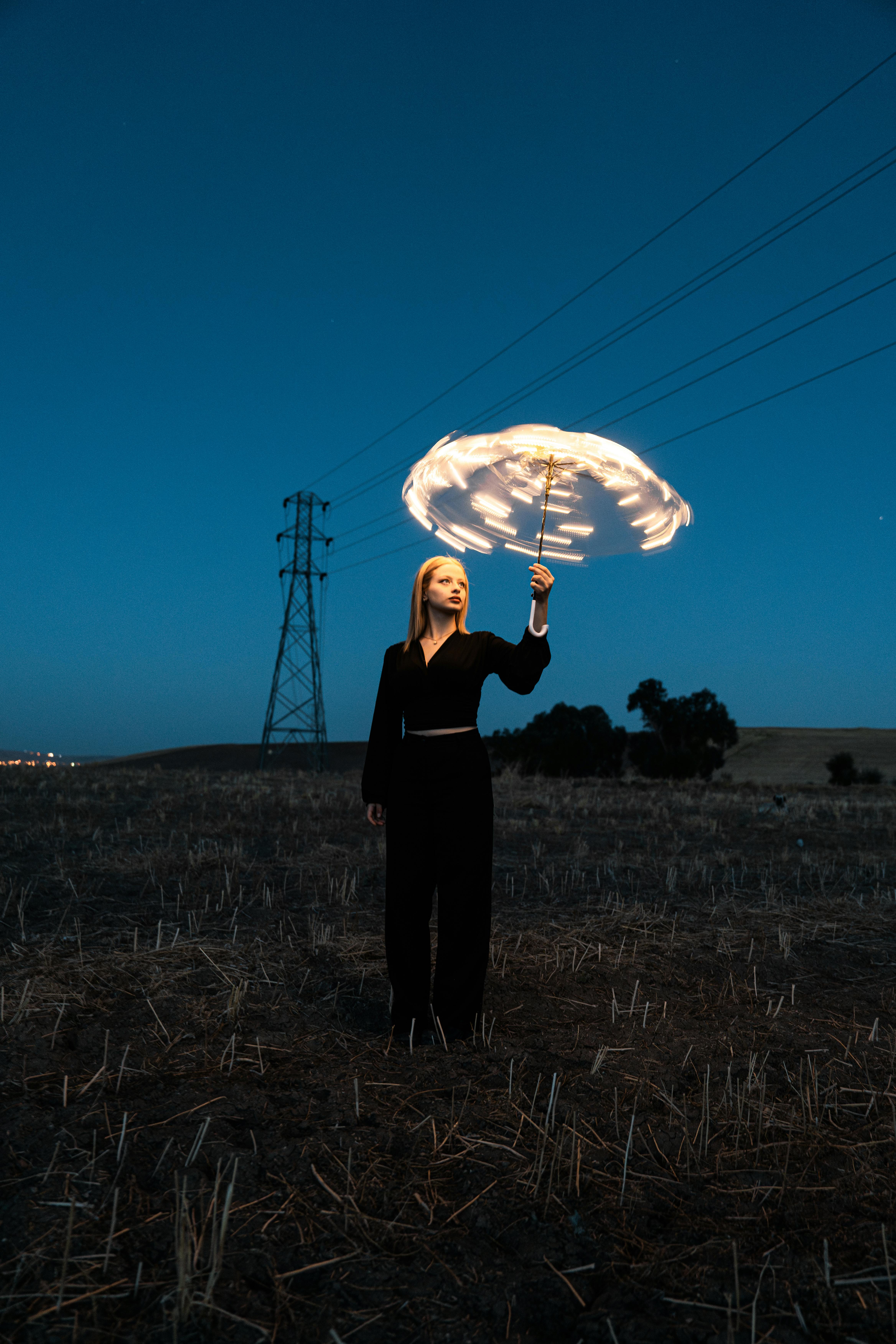 Model in Black Blouse and Pants Posing with a Illuminated Umbrella on a ...
