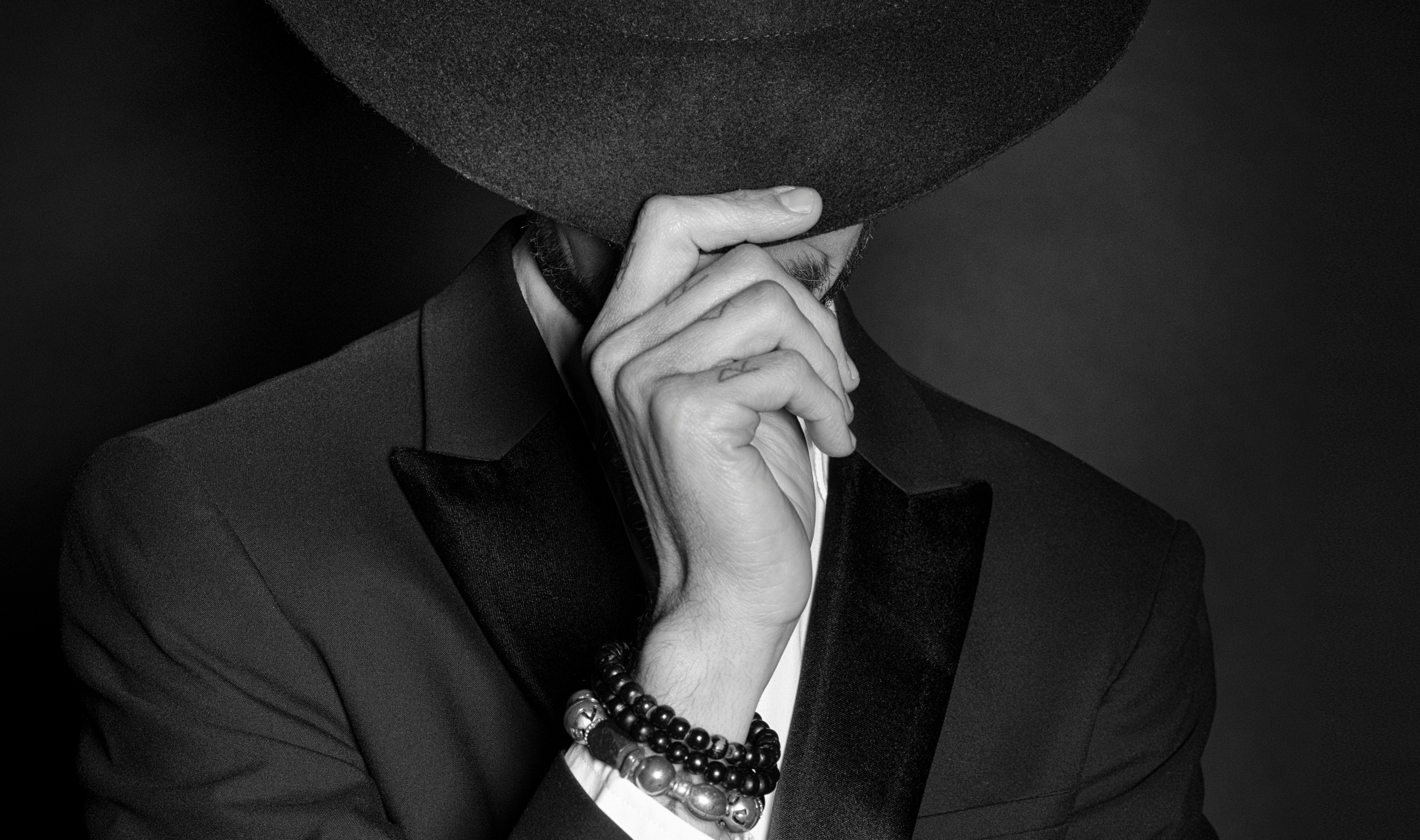 A man in a black suit and hat covering his face · Free Stock Photo